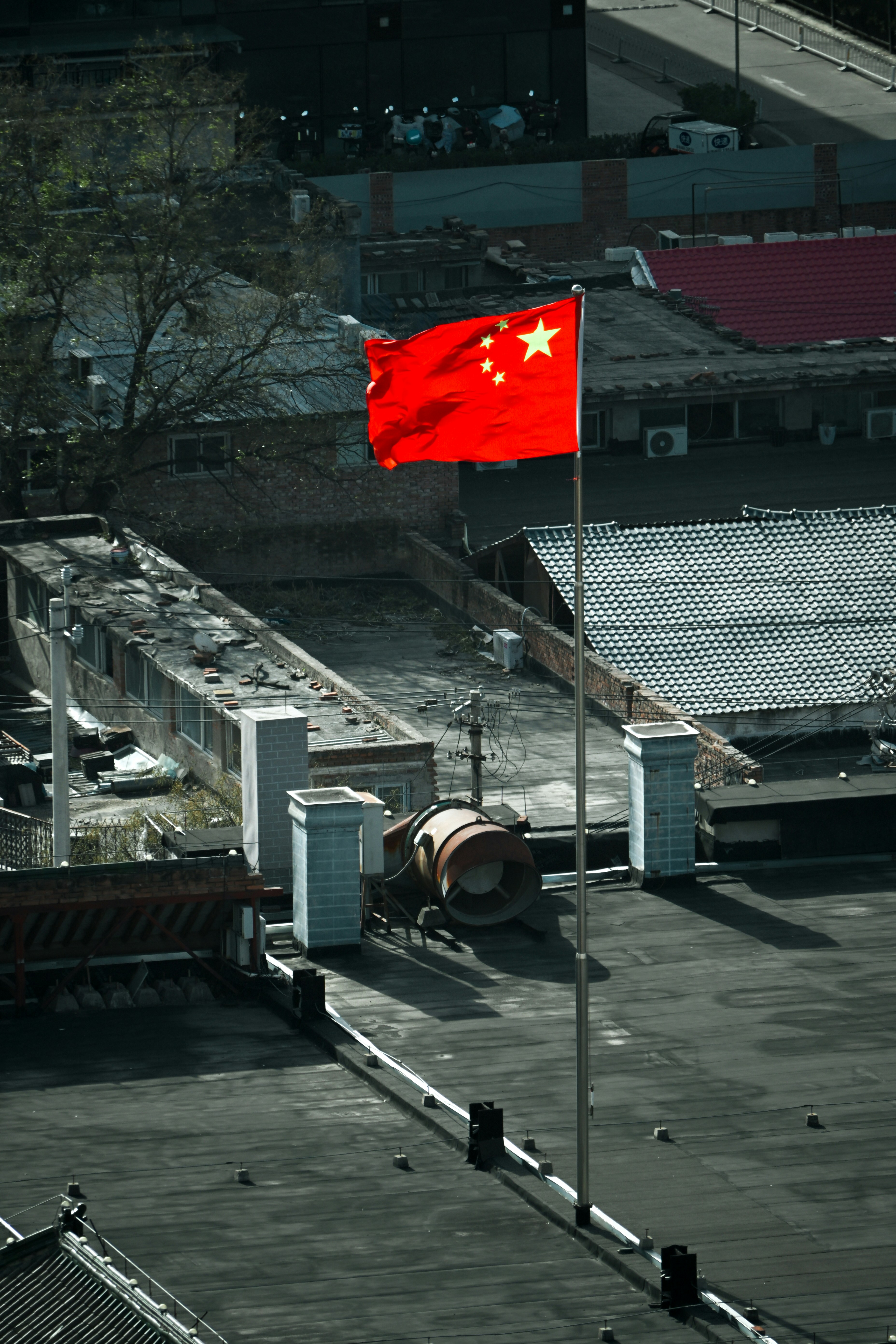 A chinese flag waves on a flagpole over cityscape.
