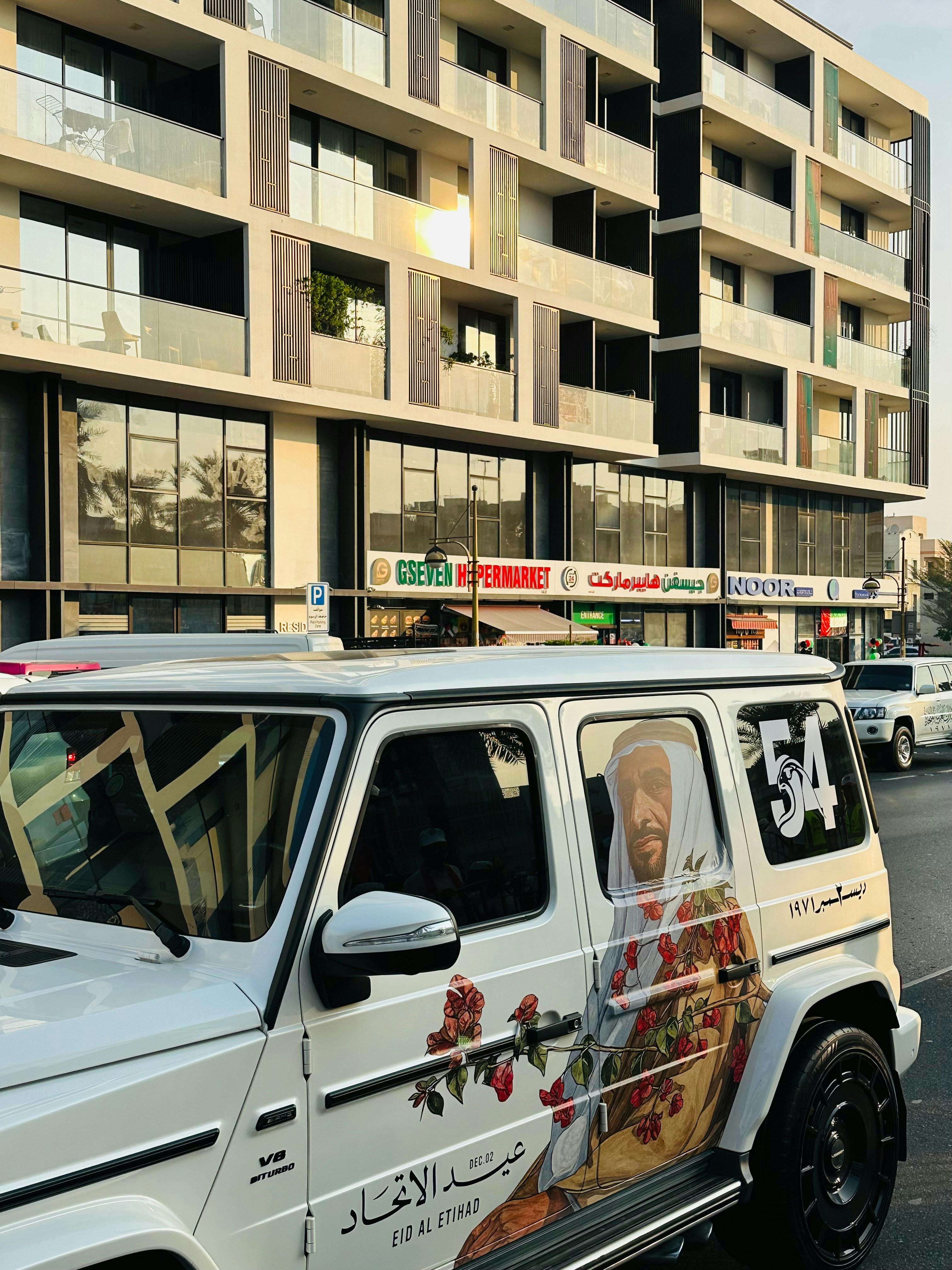 Portrait on Wheels: A White SUV with Floral Art Passing a Modern Building