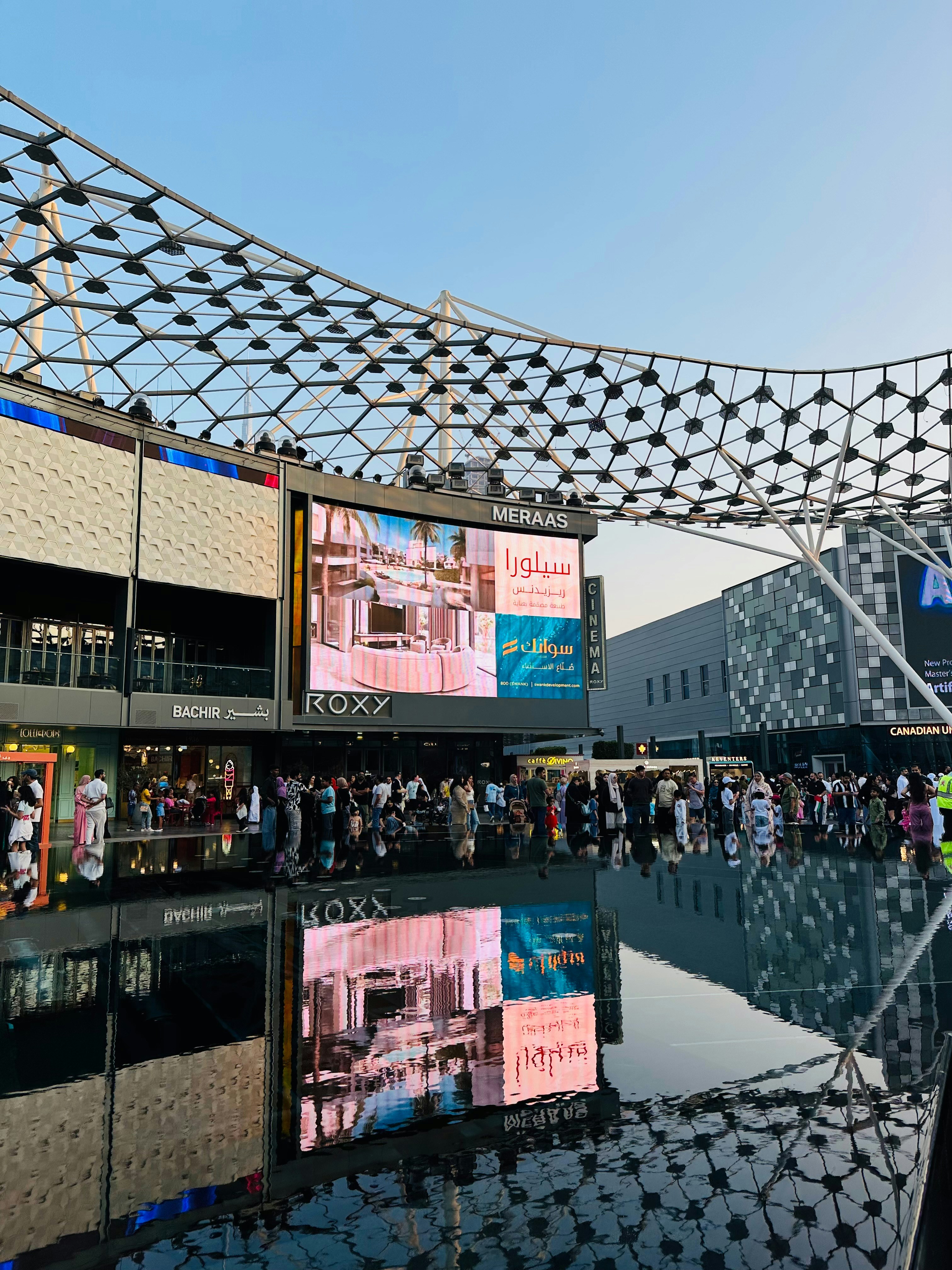 Mirror Plaza: Crowd and Digital Screen Framed by a Latticed Canopy