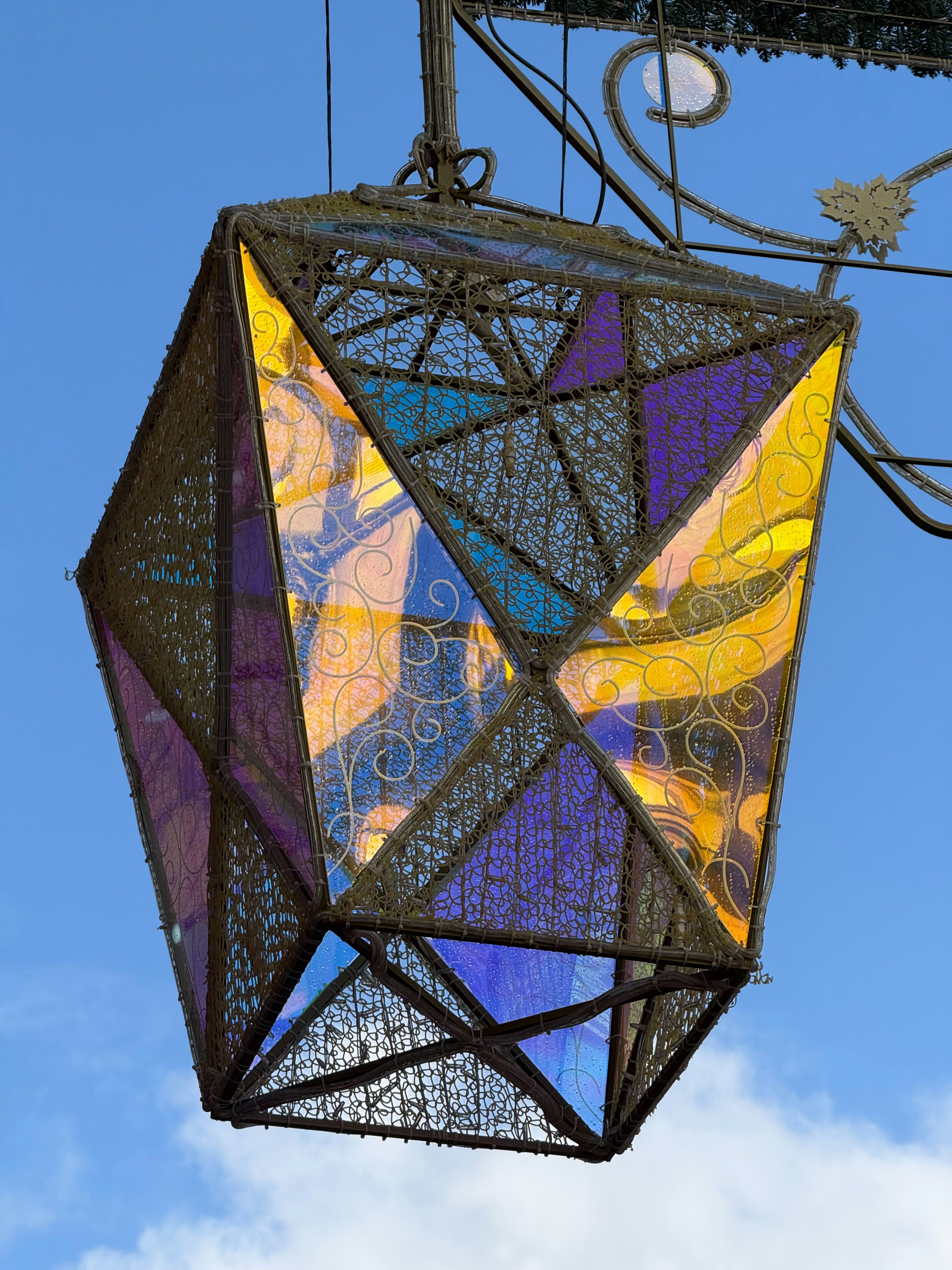 Stained lantern in a geometric web of iron and color against a bright sky