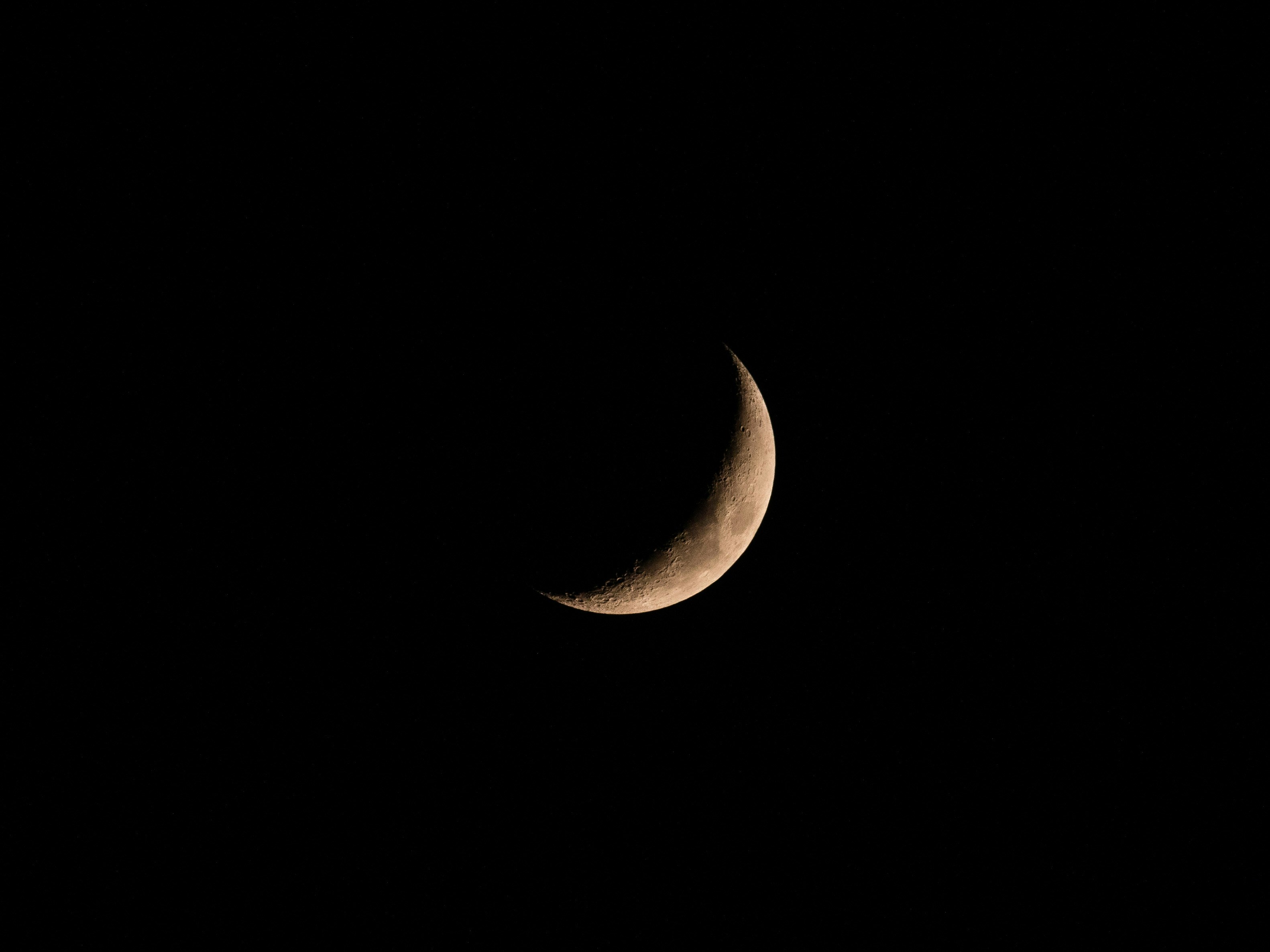 A sharp view of the crescent moon glowing in the dark night sky, showing its curved shape and detailed surface as it hangs quietly above the horizon.