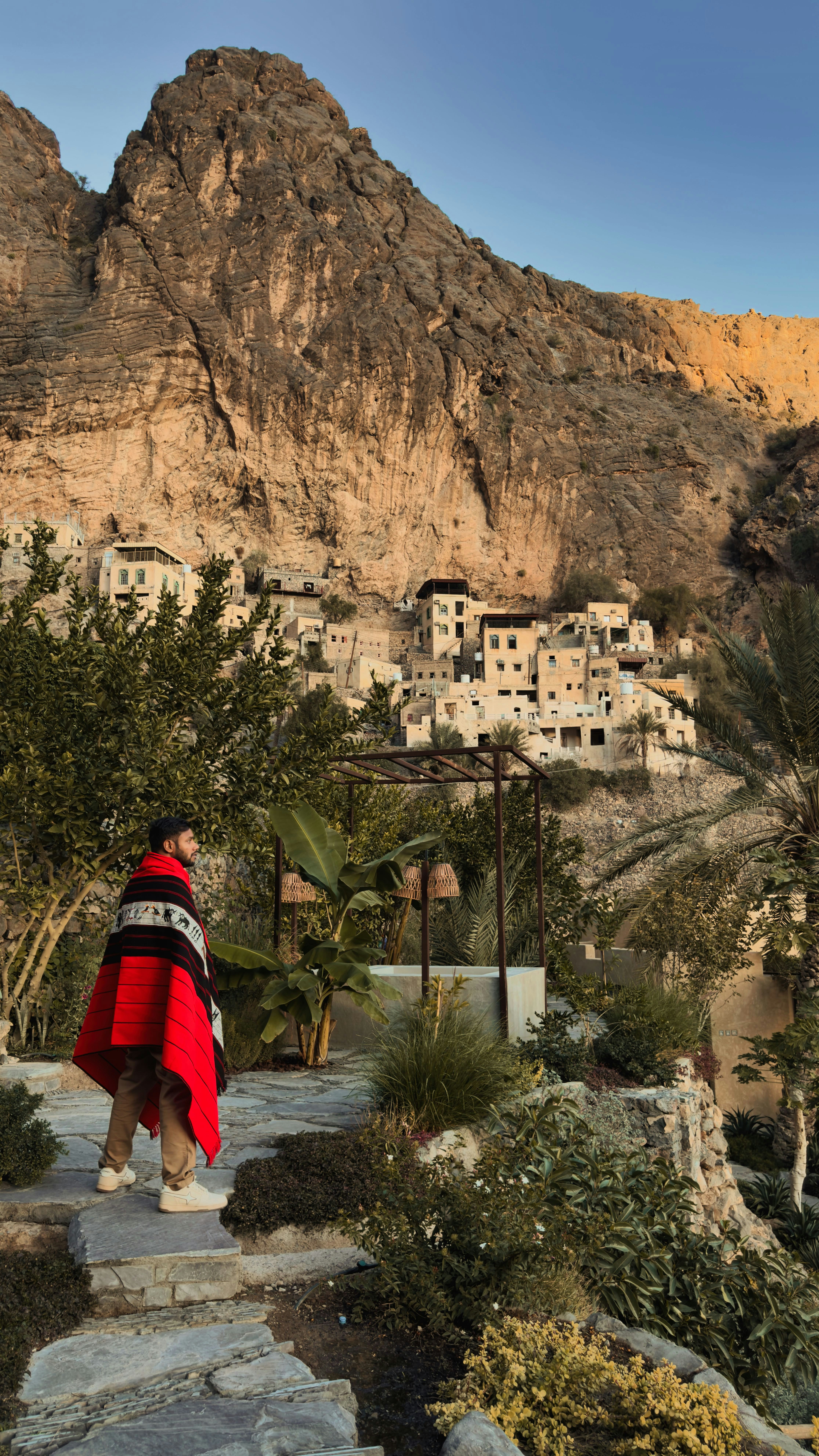 Red-cloaked wanderer at the foothills of sunlit cliffs
