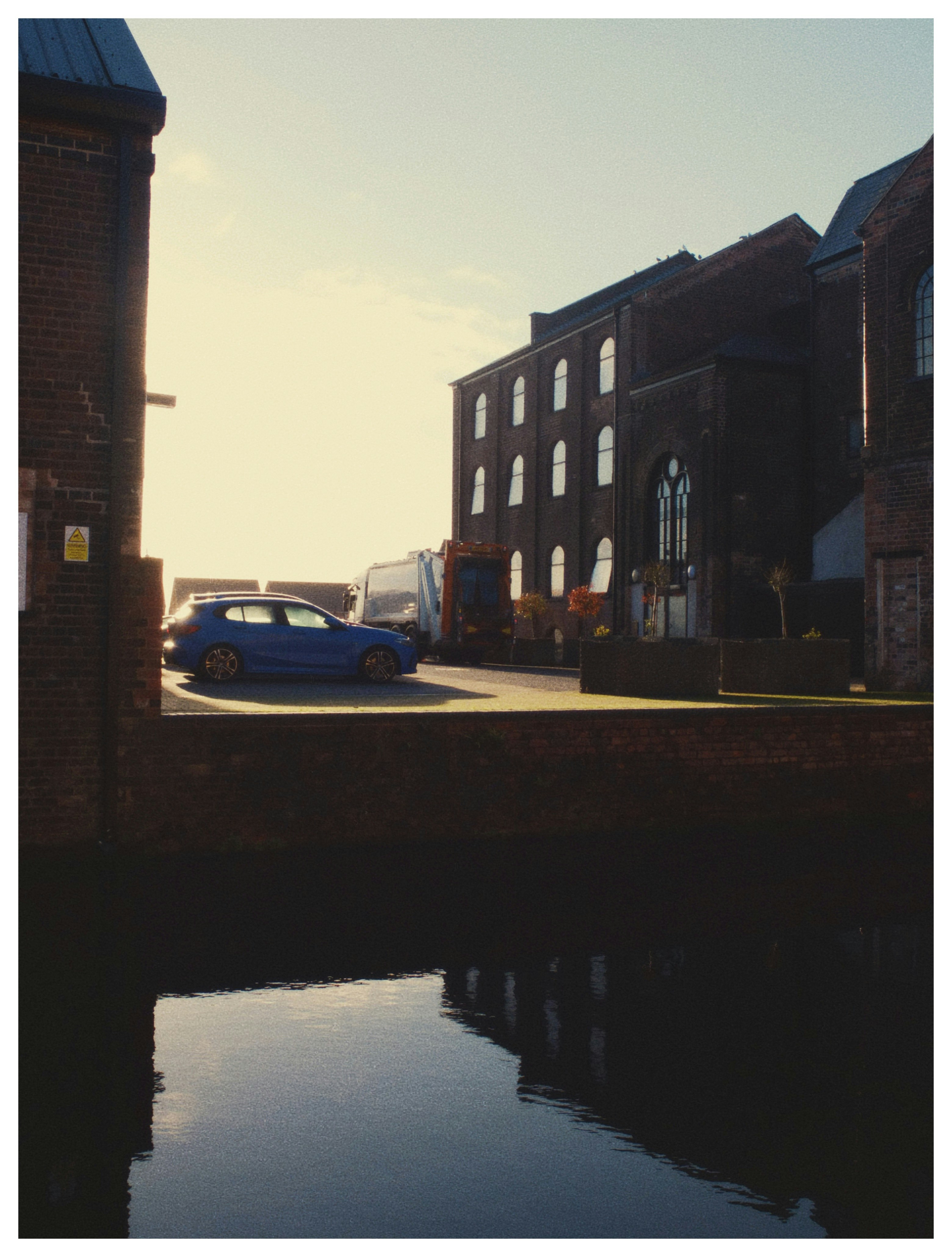 Blue compact car at the quay: sunlight over brick warehouses