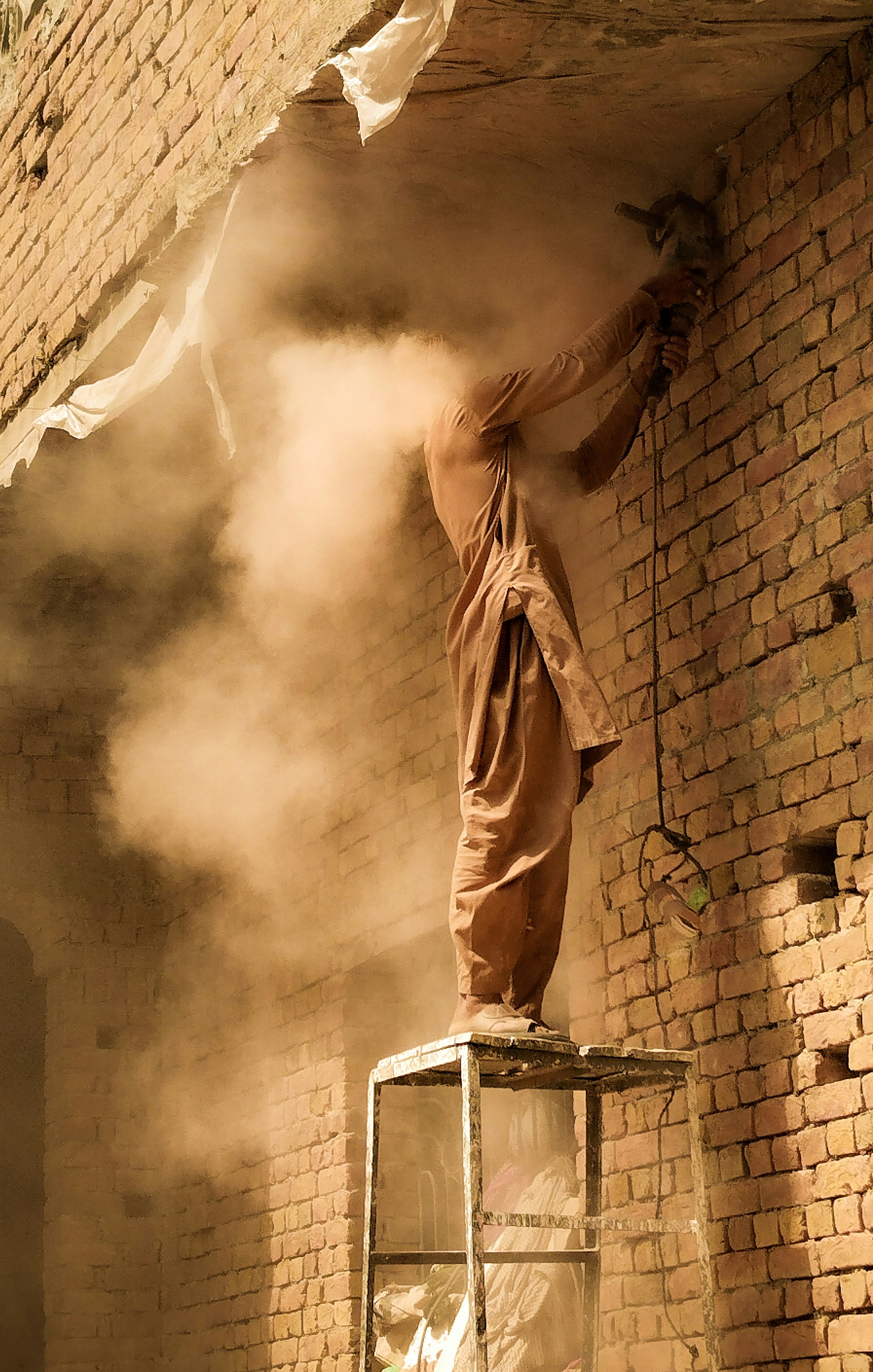 Worker cutting brick wall creating dust cloud
