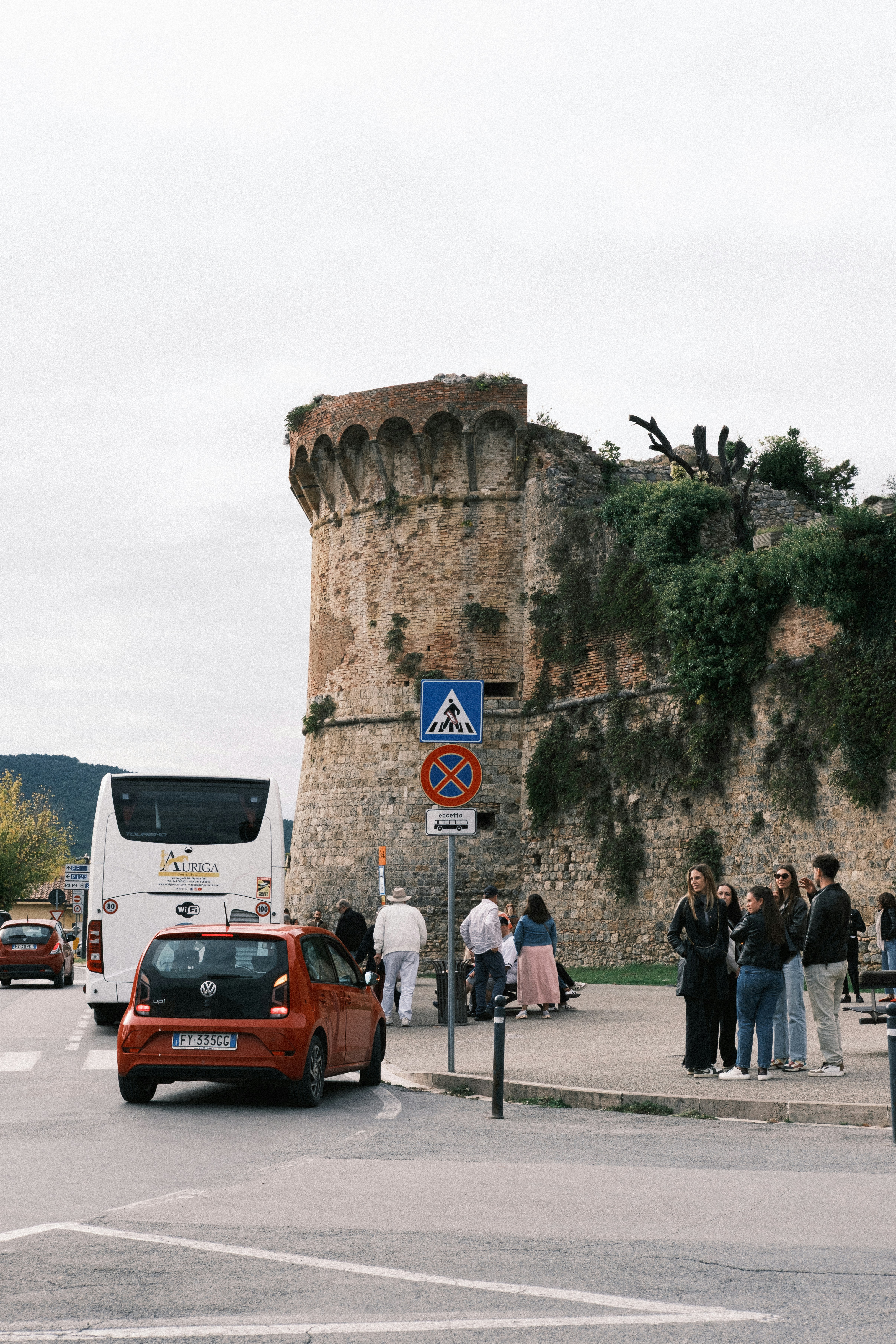 Tourists converge at the ancient wall as a red hatchback waits at a crosswalk