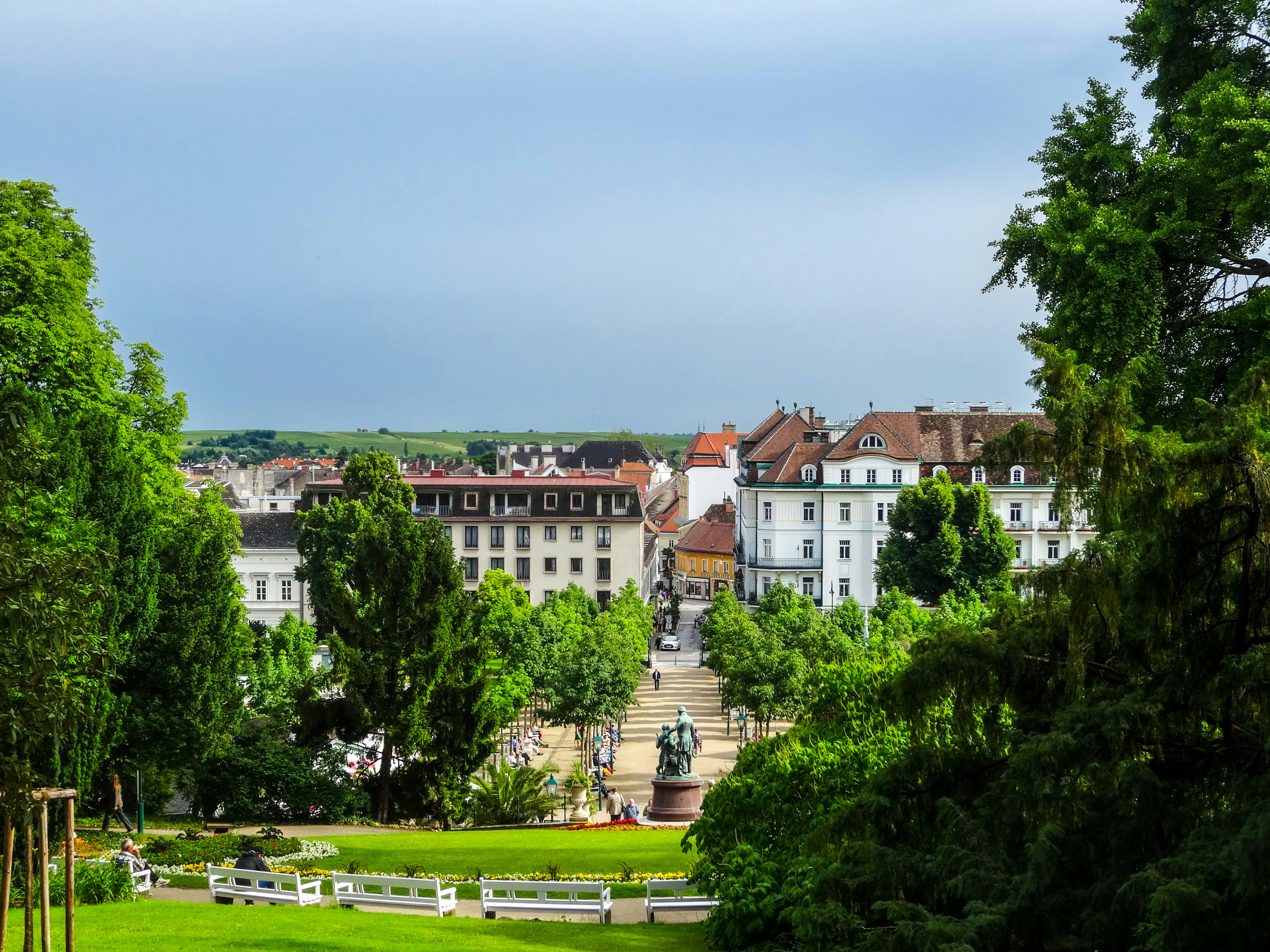 A quiet European plaza unfolds between canopy and city rooftops