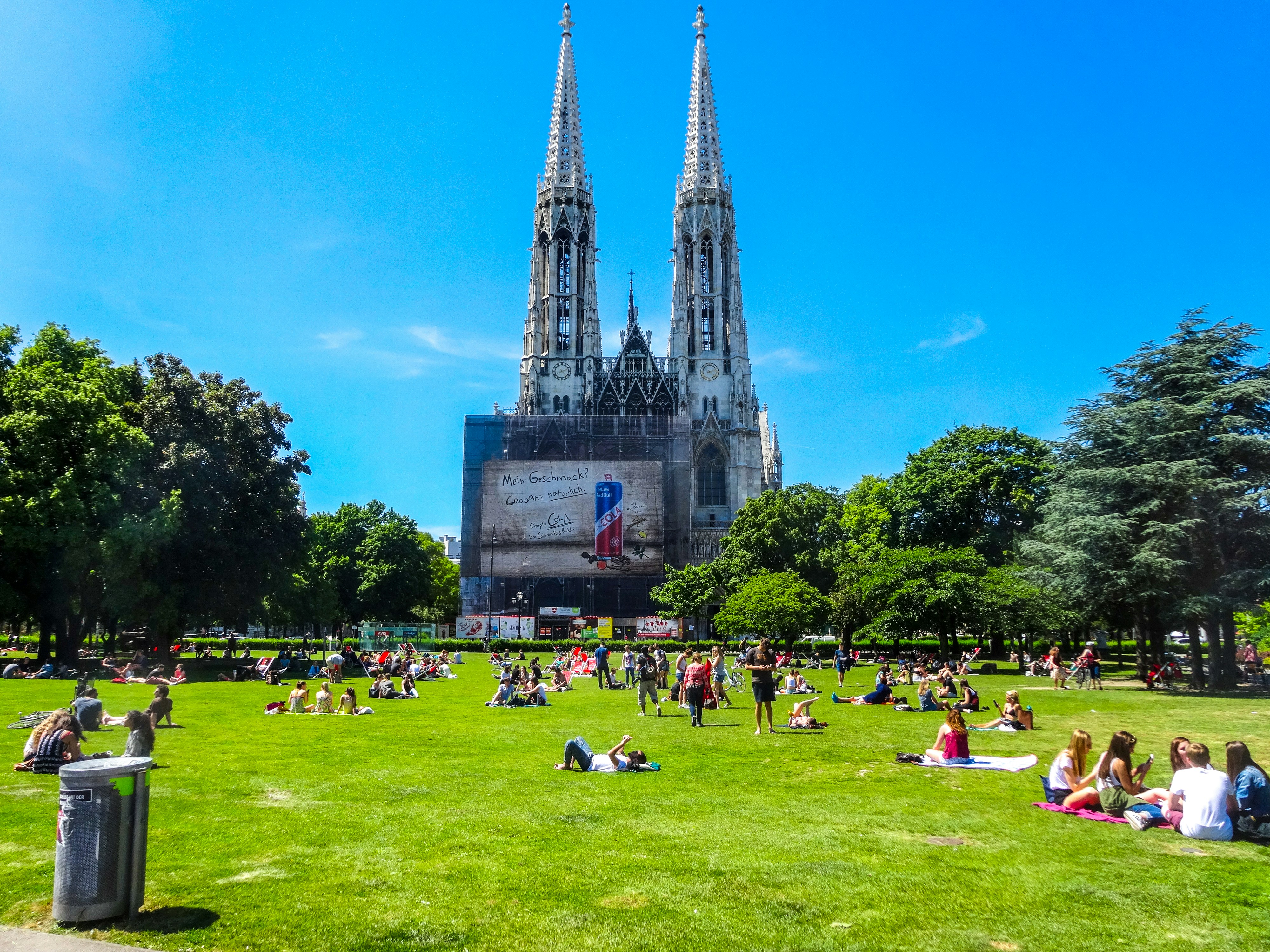 People relaxing on grass in front of a large cathedral.