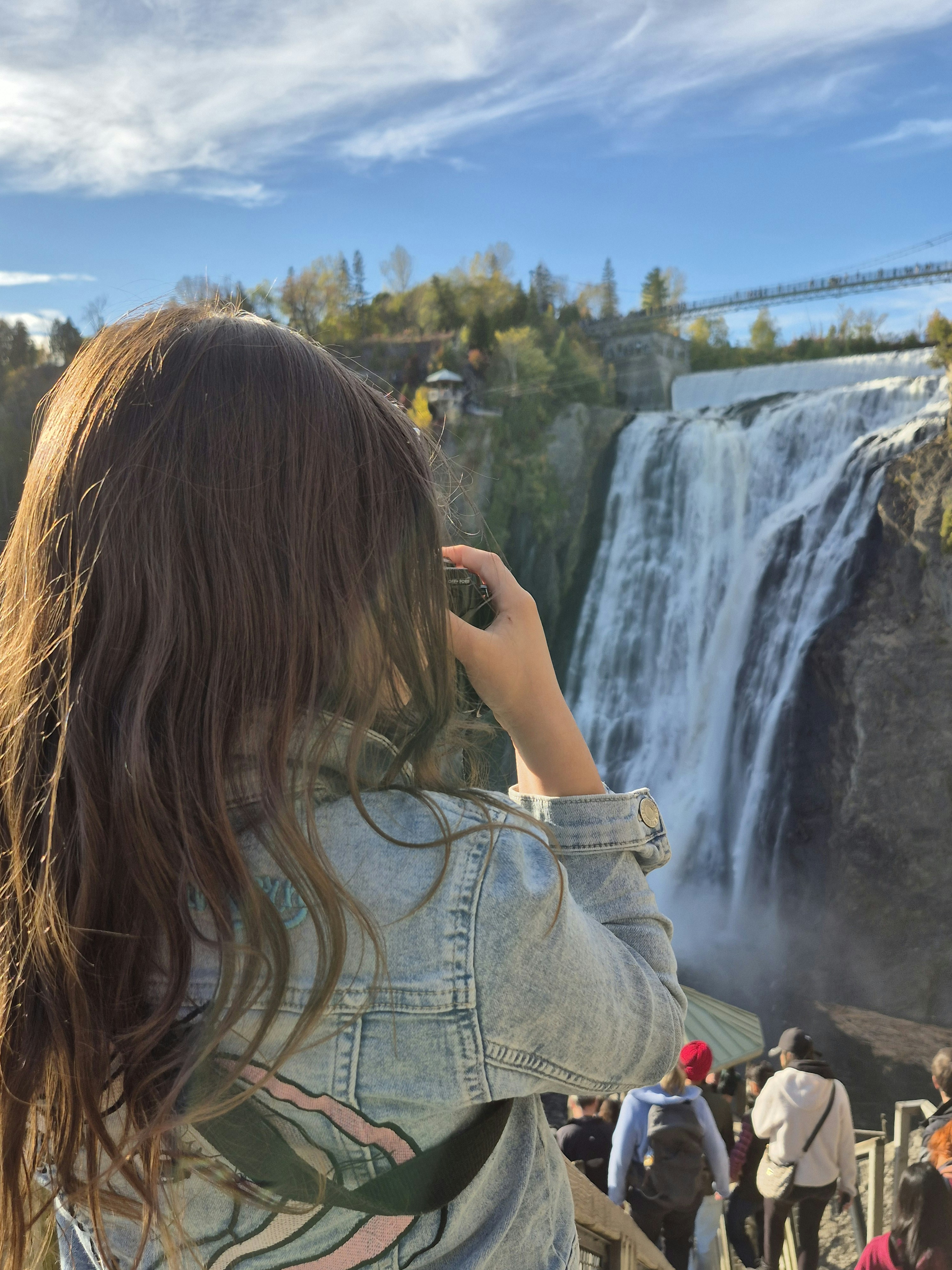 Woman takes picture of large waterfall with people below