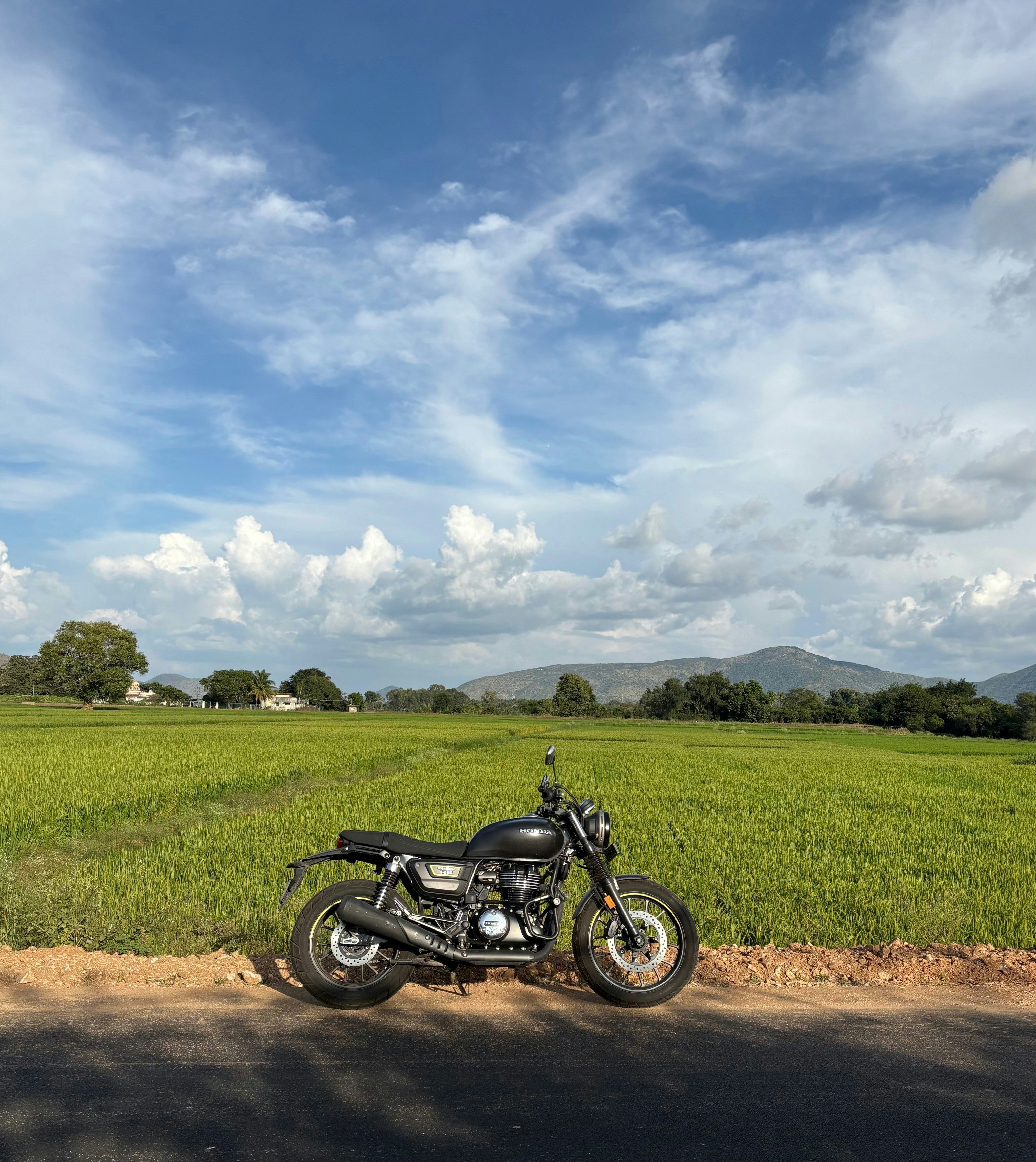 Motorcycle at the Edge of a Green Field Under a Sky of Puffy Clouds