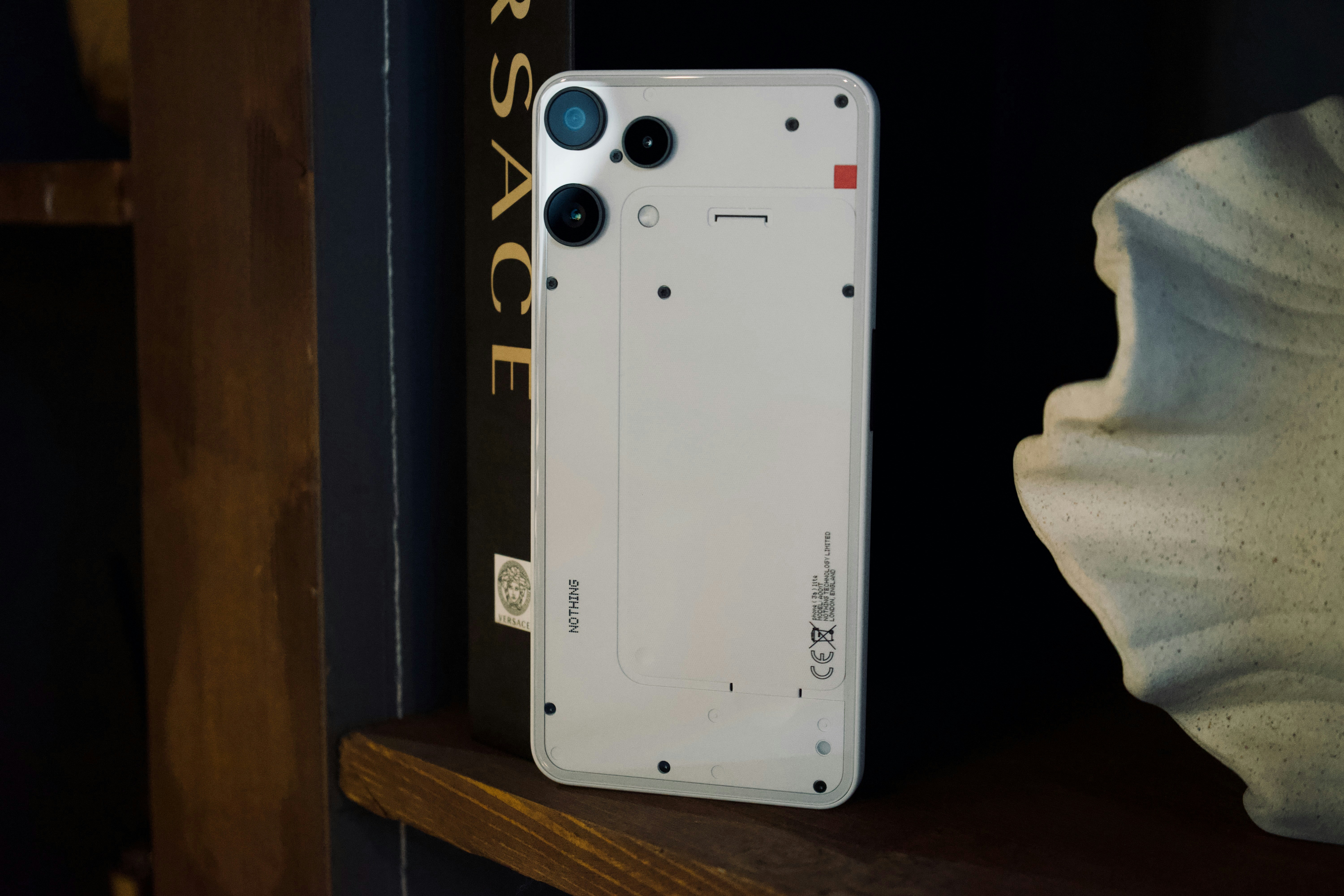 White OnePlus-esque smartphone resting on a dark wooden shelf