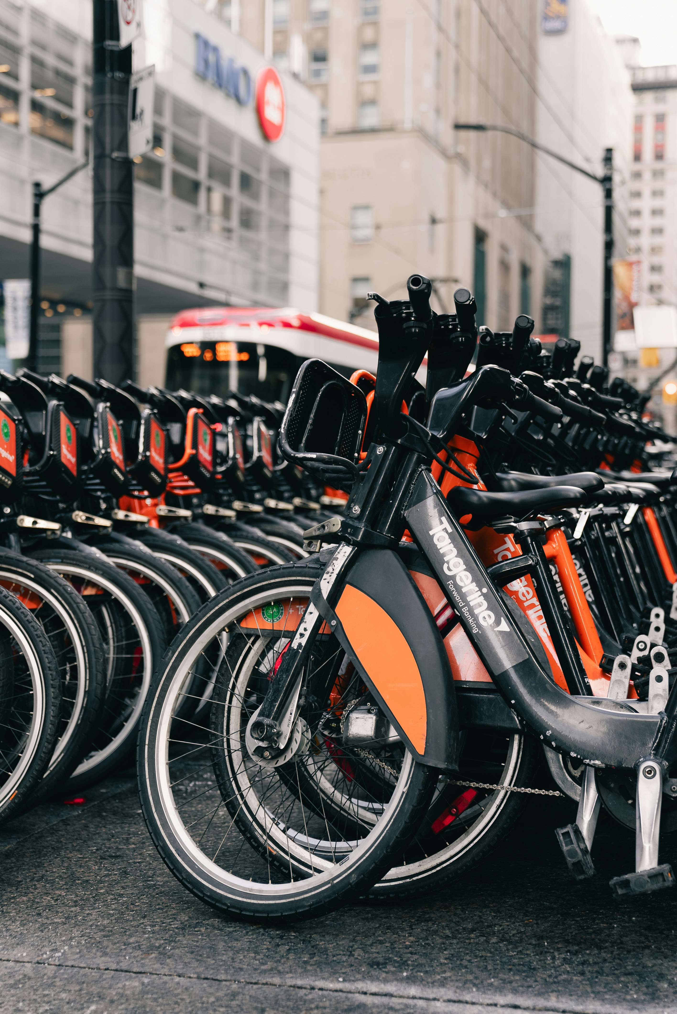 Line of Orange-Covered City Bicycles Docked in a Busy Street