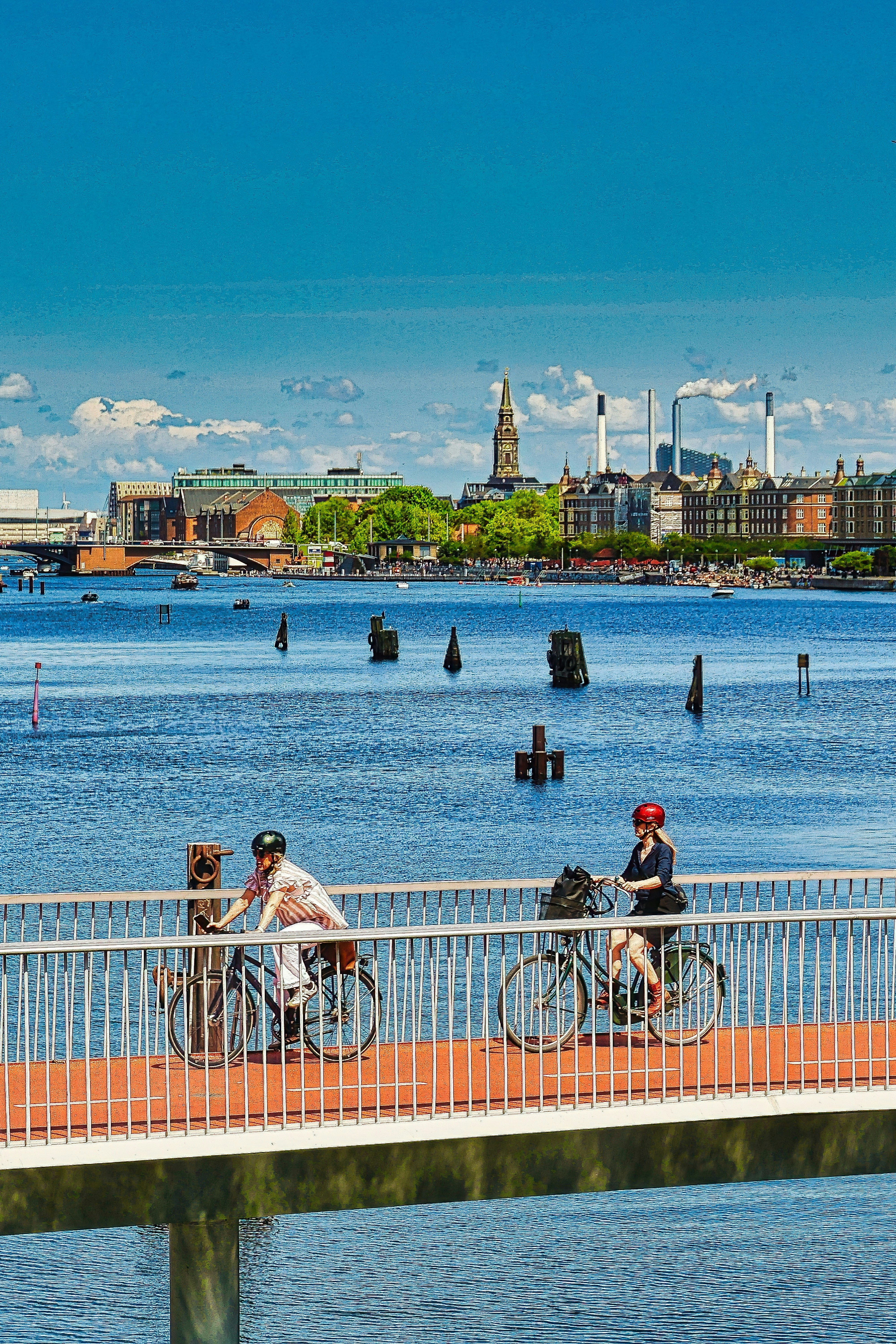 Riverside Ride: Cyclists on a Sunlit Bridge Over Calm Waters