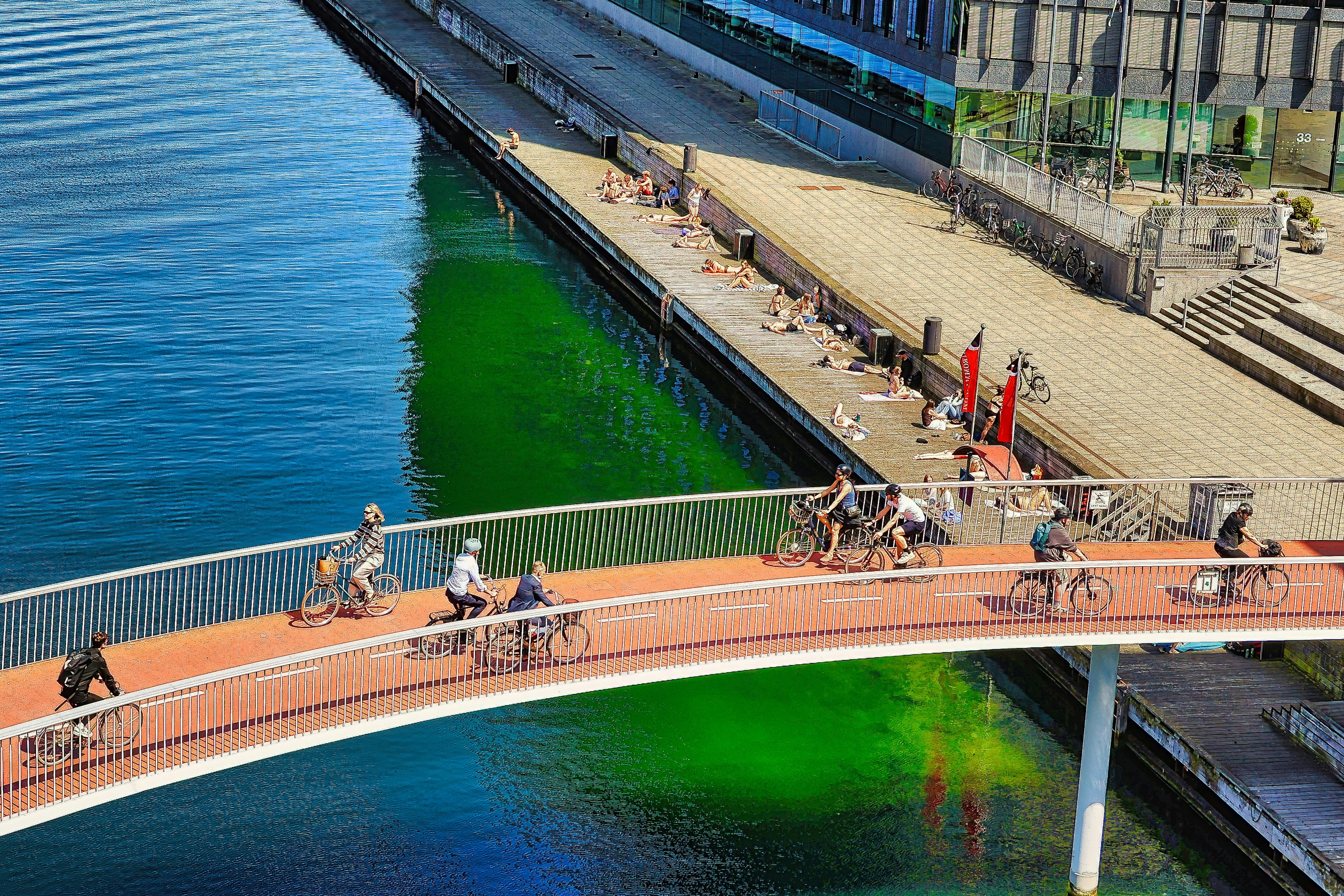 Riverside Pedestrian Arc: Cyclists Crossing a Colorful Bridge
