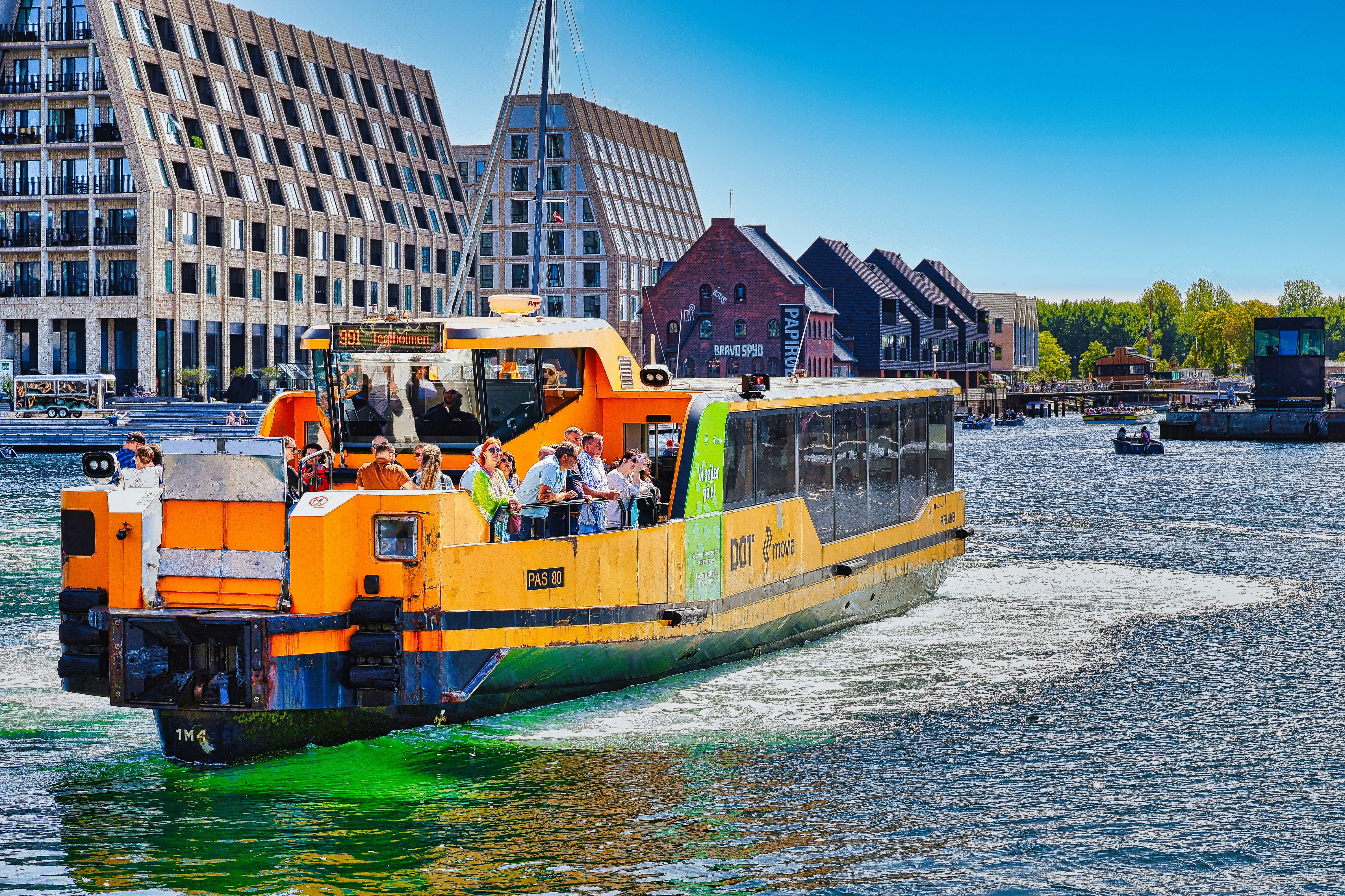 Orange ferry cuts through a sunlit urban canal