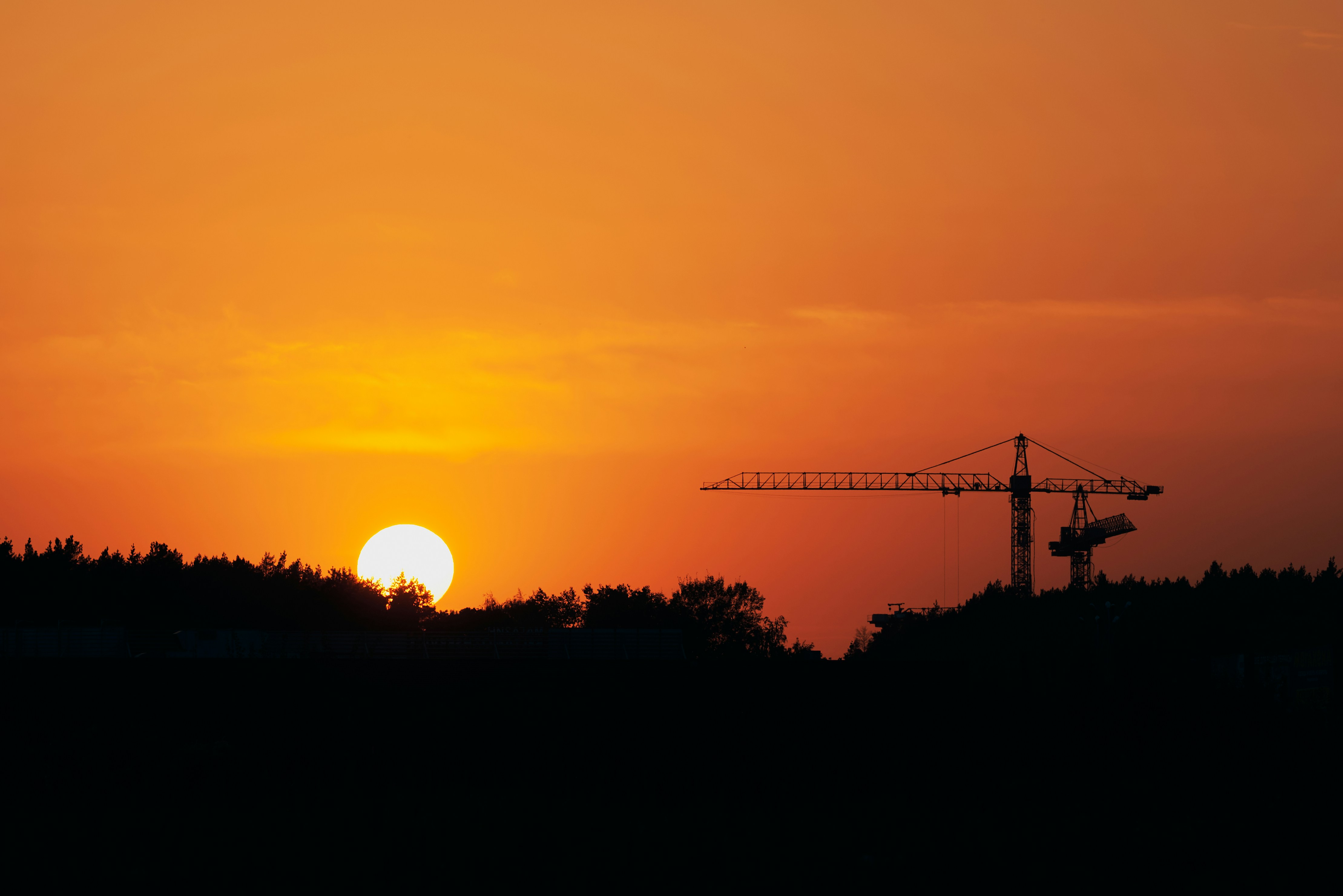 Orange Sun Dips Behind Silhouette: Construction Crane at Dusk