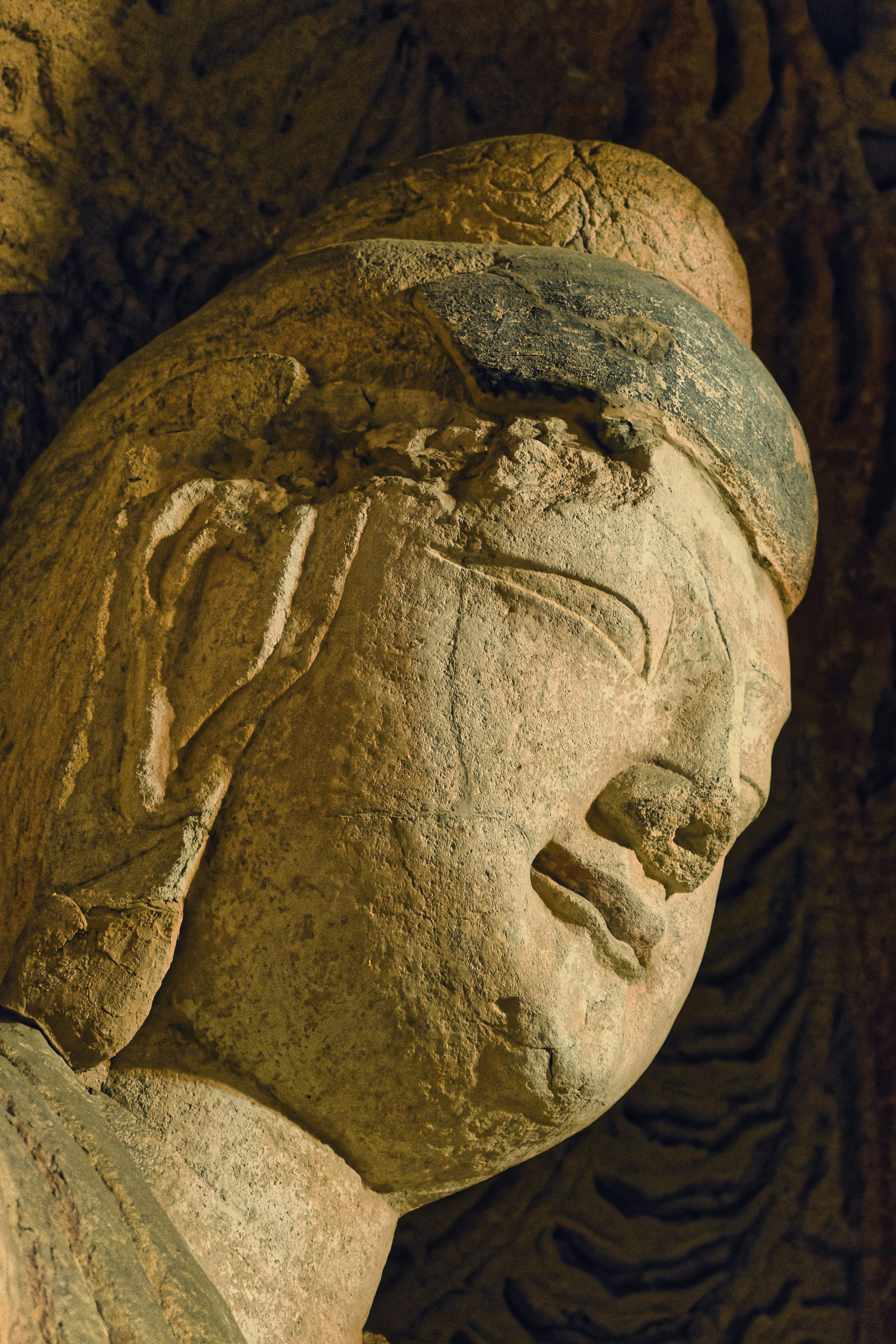 Ancient stone sculpture of serene figure located in historical cave temple, illuminated by soft light - This scene features a close-up of a carved stone statue with a calm expression, highlighting intricate details. The artwork is found inside an ancient cave temple, attracting visitors.