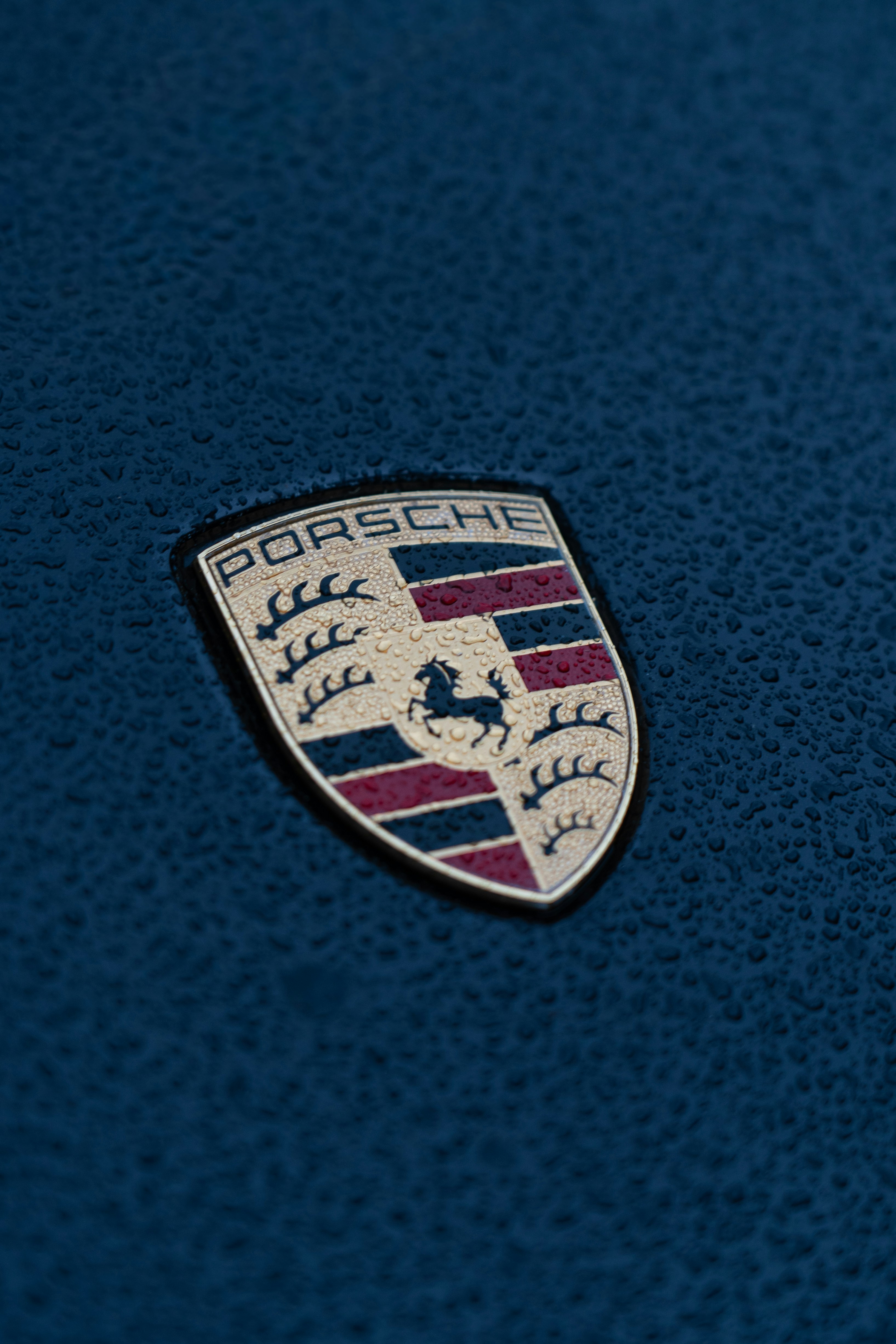 Emblem in the Rain: Porsche Crest on a Rain-Speckled Blue Surface