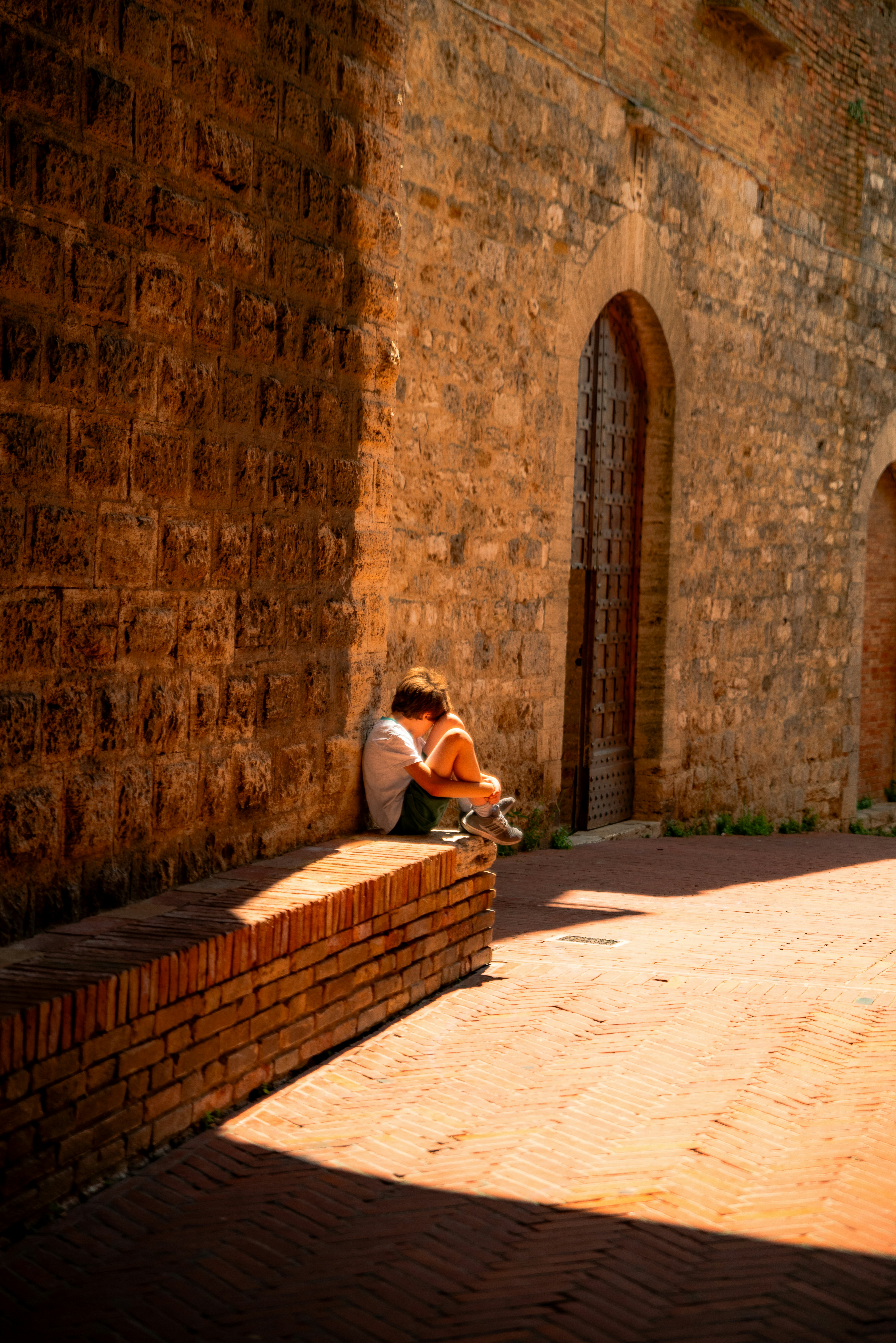 Sunlit Solitude: A Teenager Resting Along a Brick Corridor
