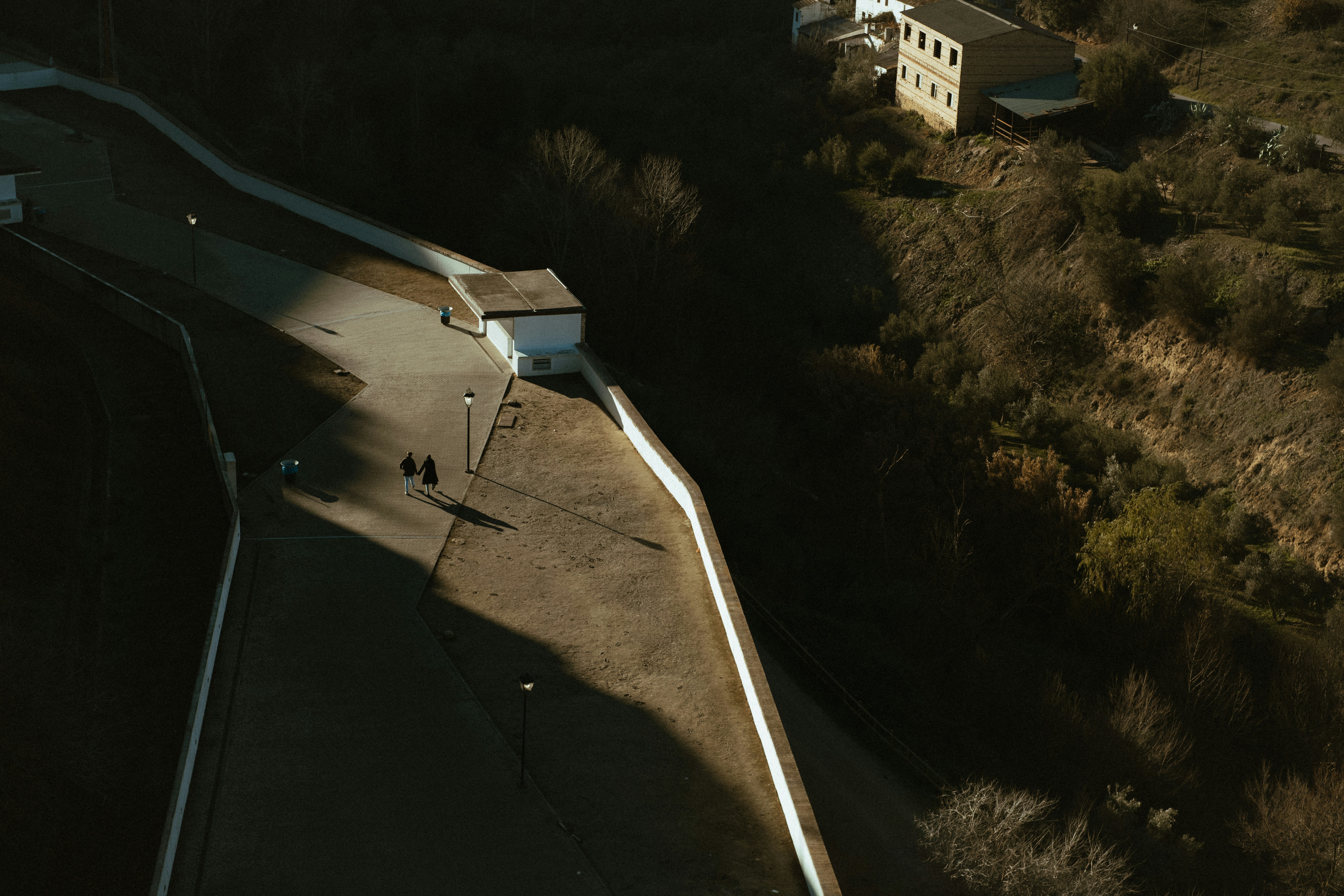 Two figures walk along a walled path beside a building. photo – Free ...
