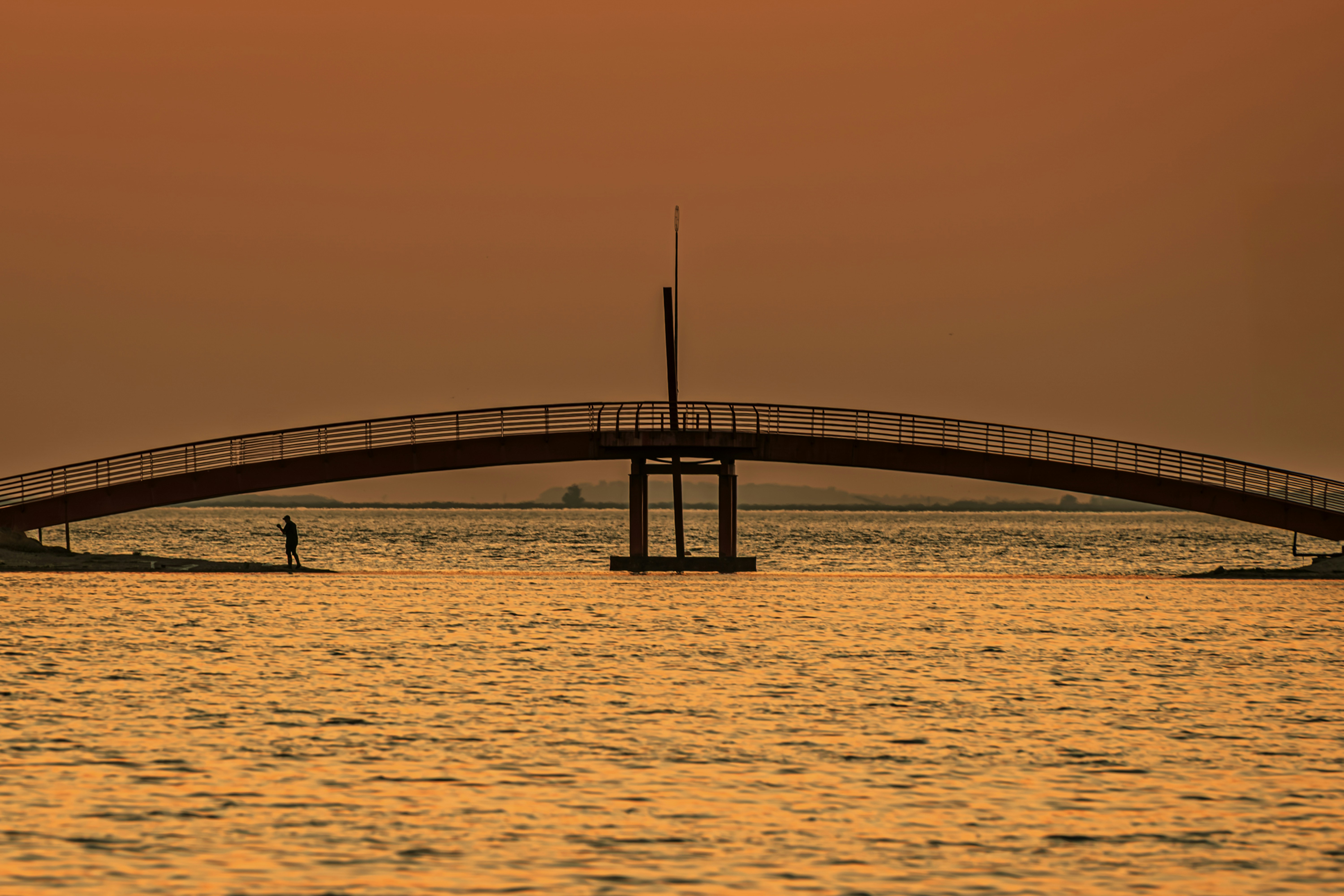 Silhouetted walker crossing the golden arch at dusk