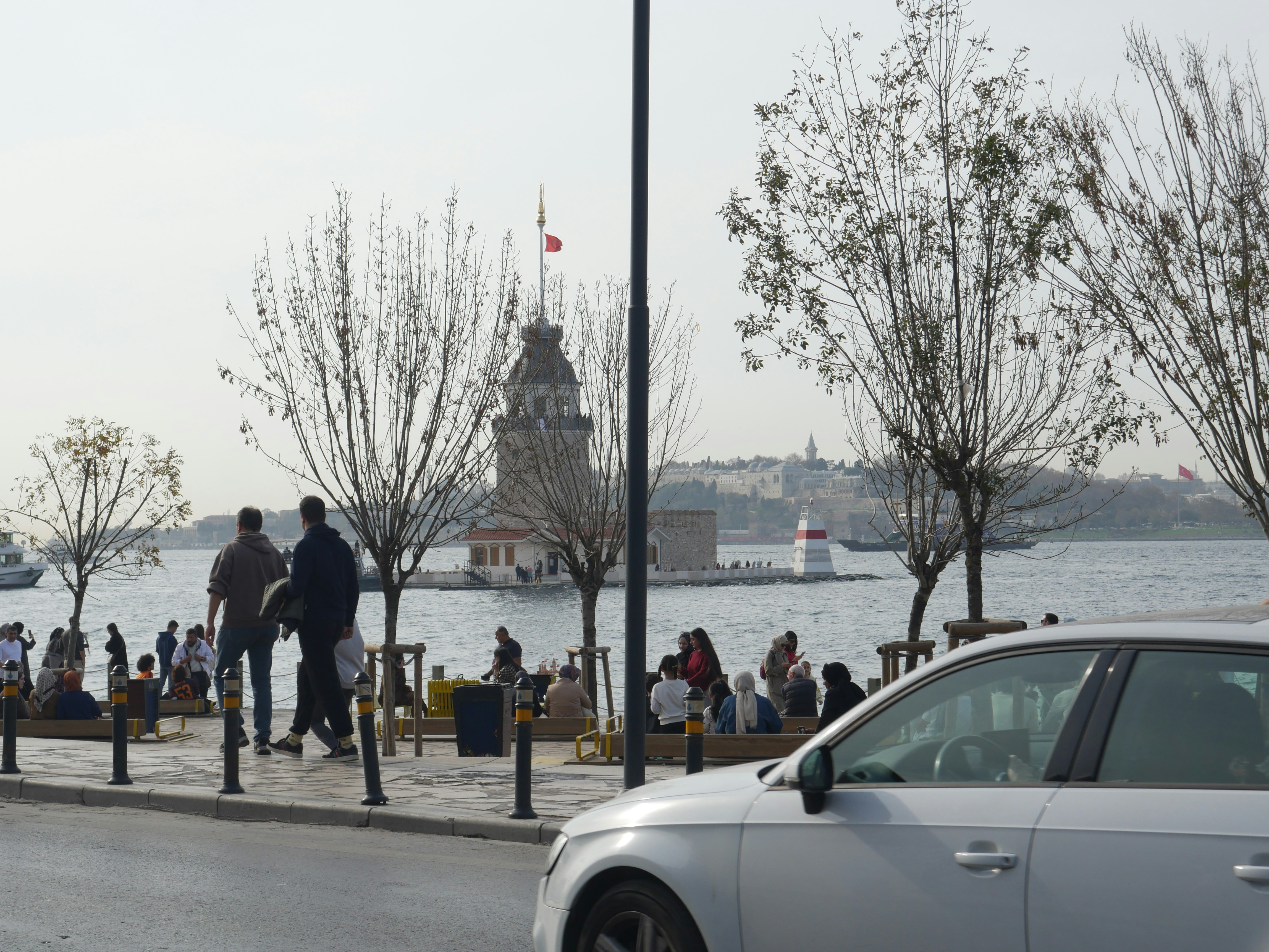 A Quiet Waterfront Promenade Framed by Bare Trees and a Silver Car