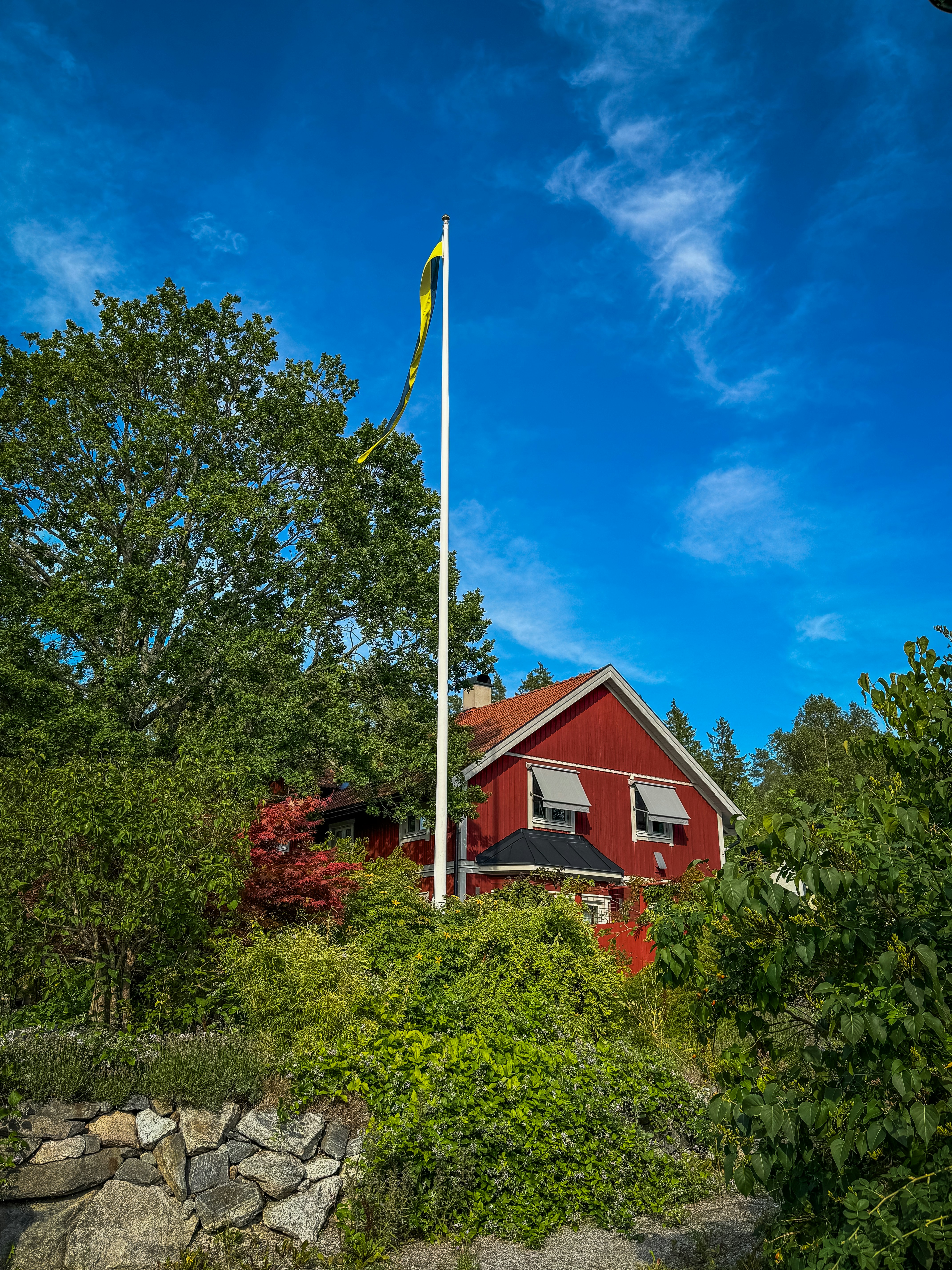 A red house surrounded by greenery, with a flag waving under a bright blue sky.