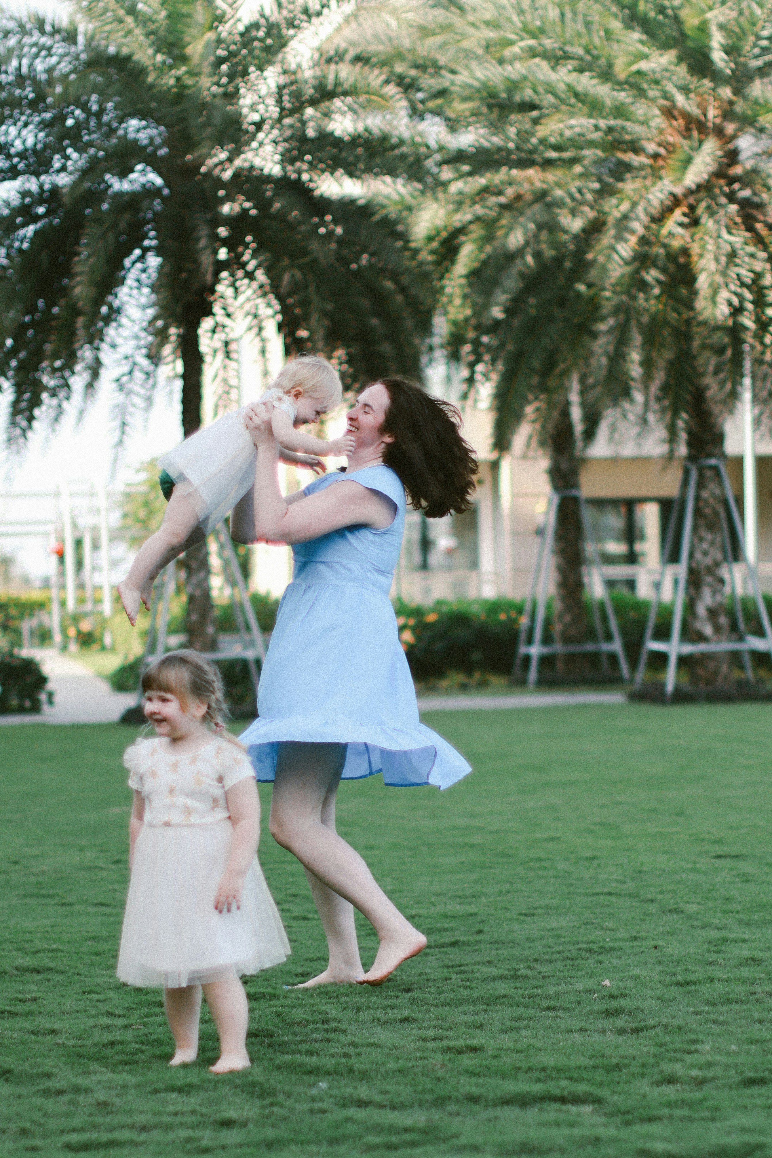 Joyful Mother Lifts Baby While Two Little Girls Play on a Sunlit Lawn
