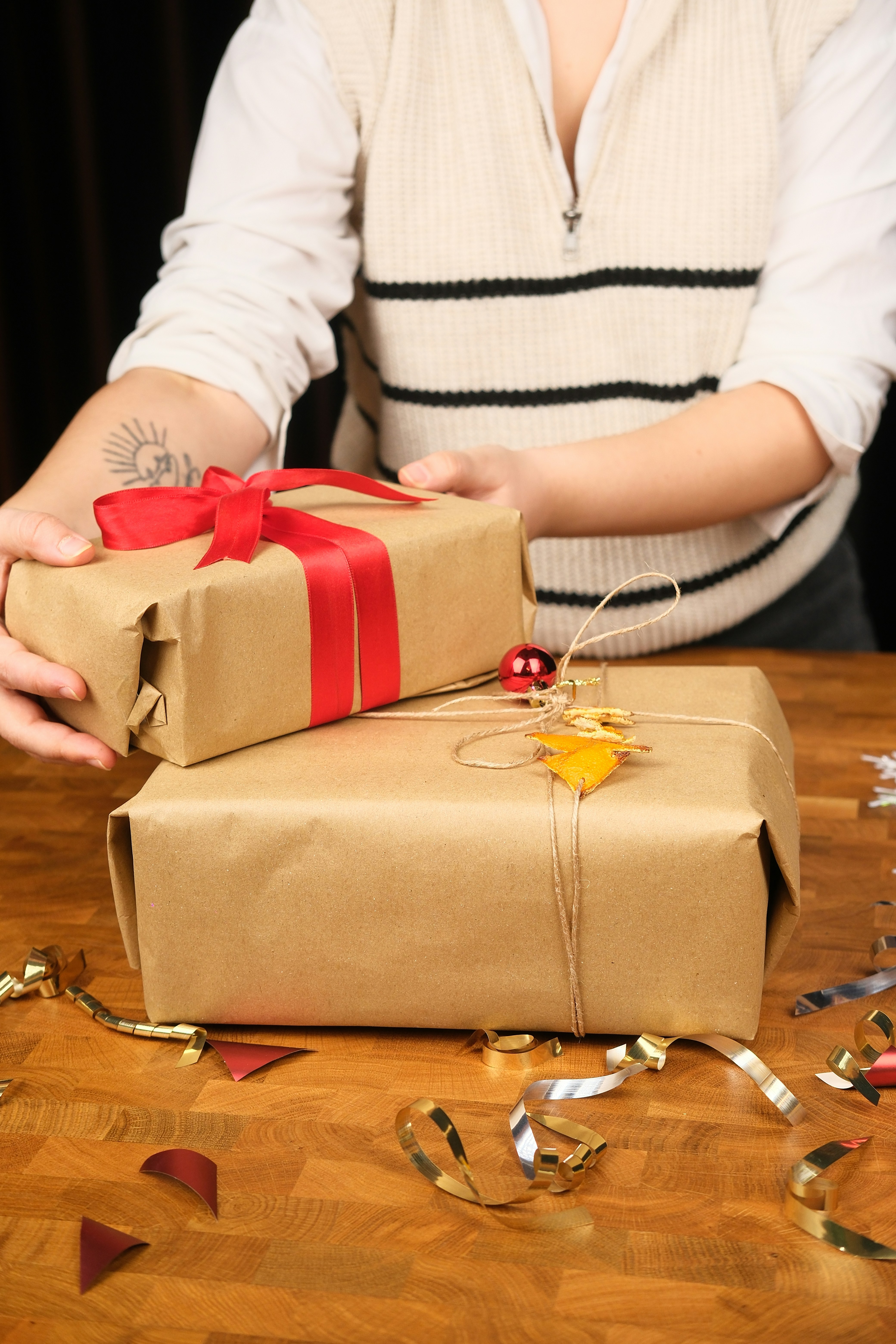 Person Holding Christmas Gifts Wrapped in Kraft Paper with Festive Ribbons