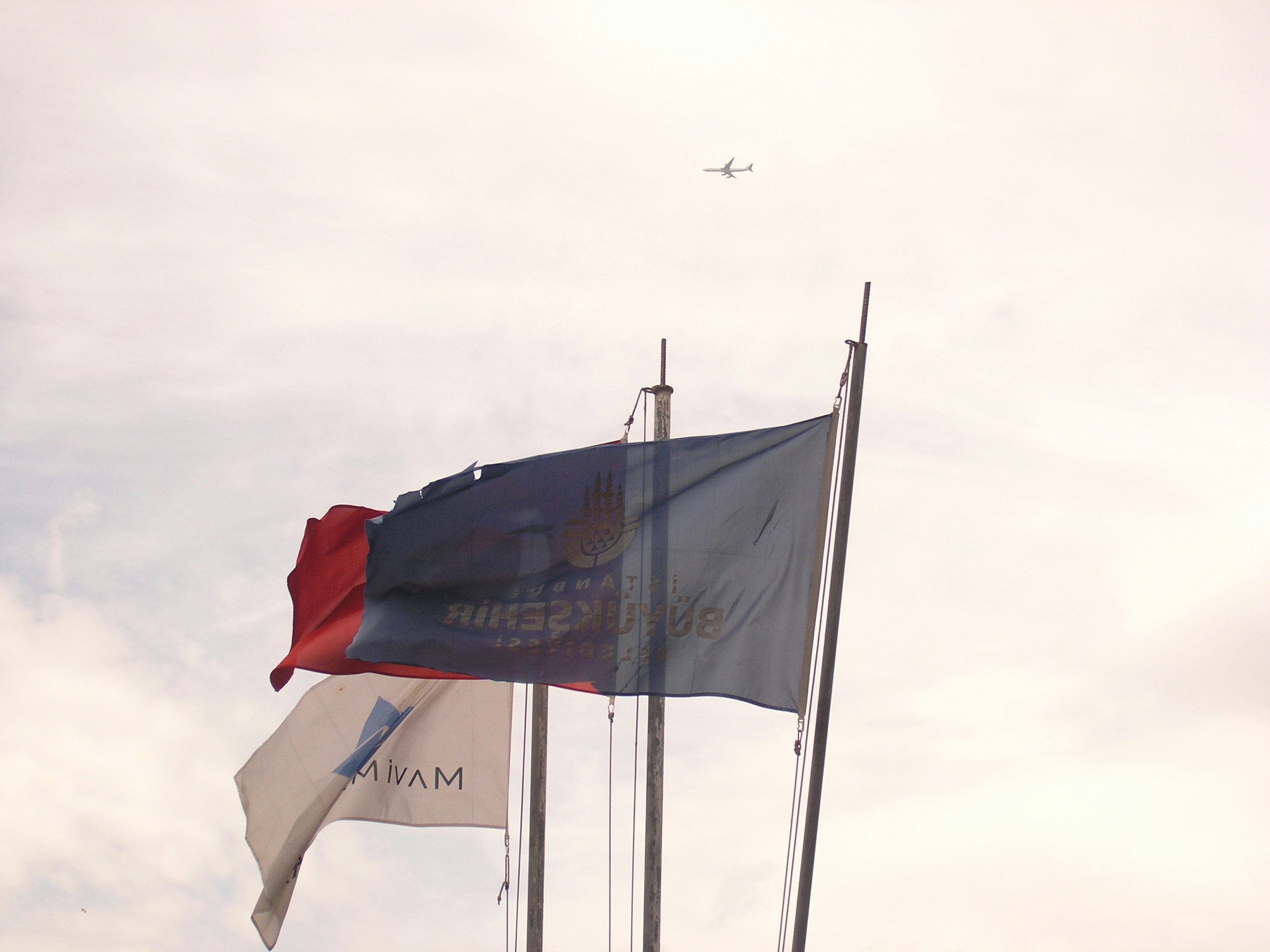 Flags fly against a cloudy sky with airplane.