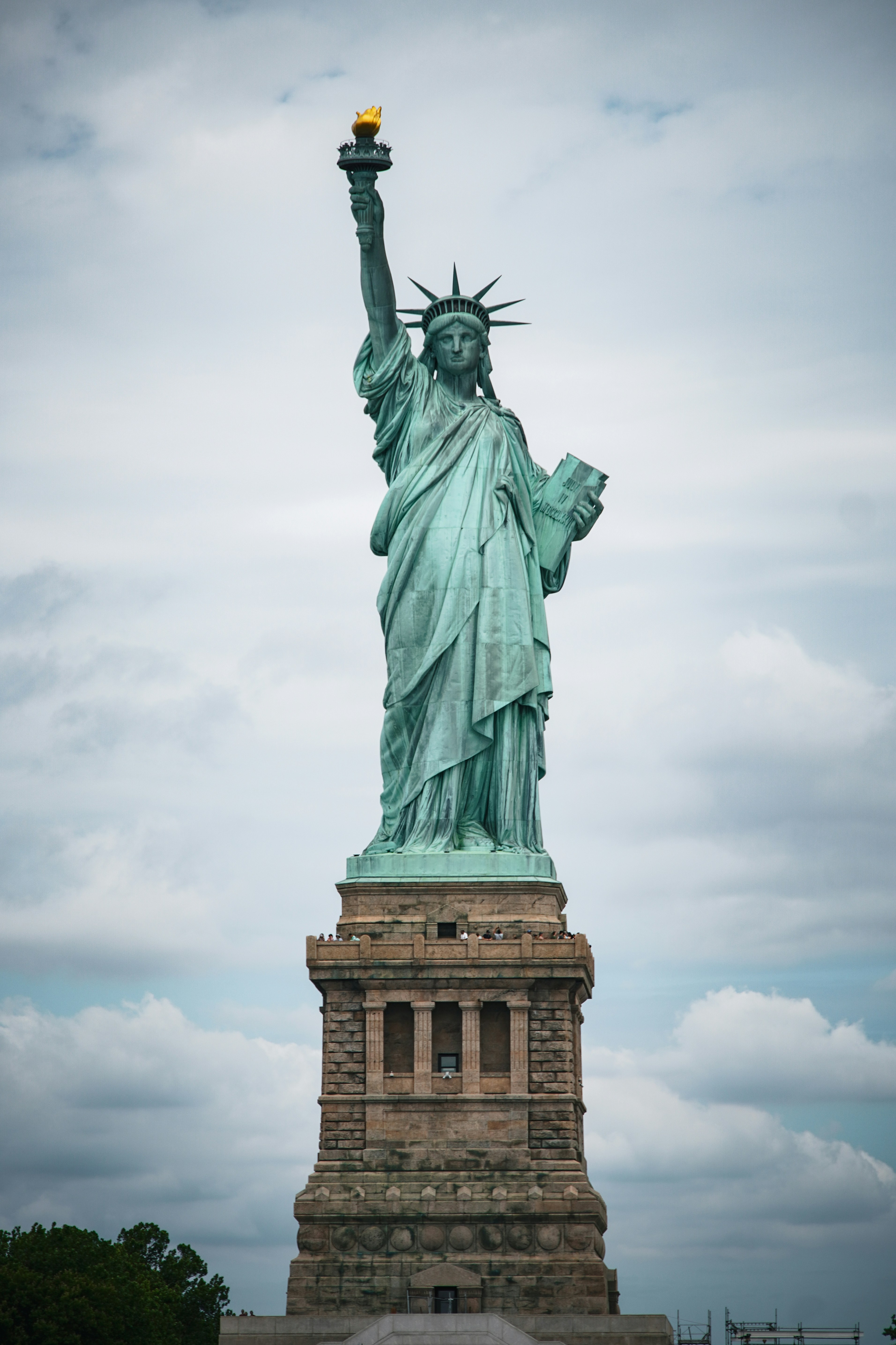 A majestic view of the Statue of Liberty standing tall on Liberty Island in New York City. Captured from a low angle, the iconic monument rises against a cloudy sky, showcasing its historic architecture and symbolic torch. A timeless representation of freedom, travel, and American heritage.
