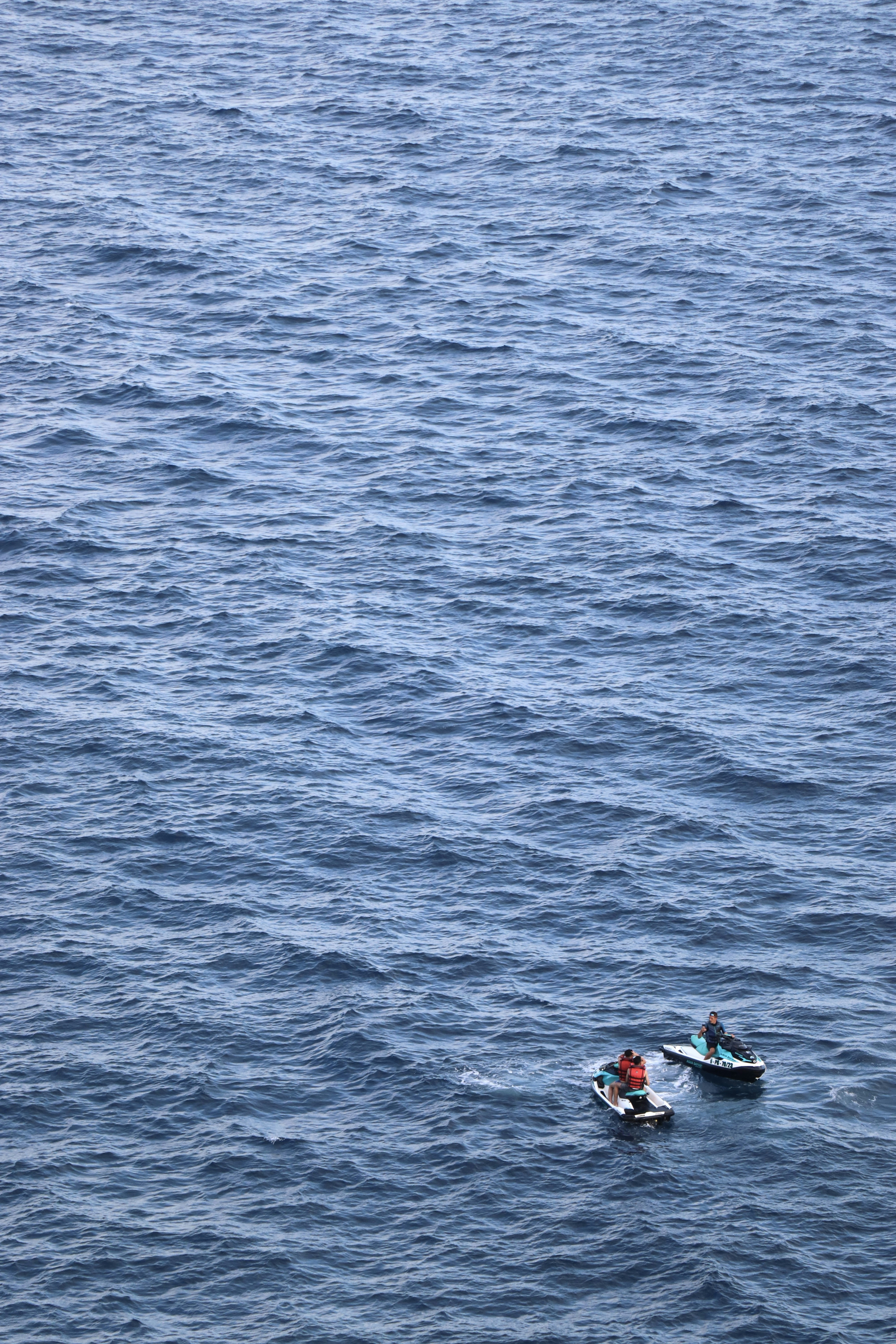 Two riders on jet skis carve small wakes across a wide field of rippled blue water. The frame is mostly ocean, using negative space to emphasize scale, motion, and the simple joy of being out at sea.