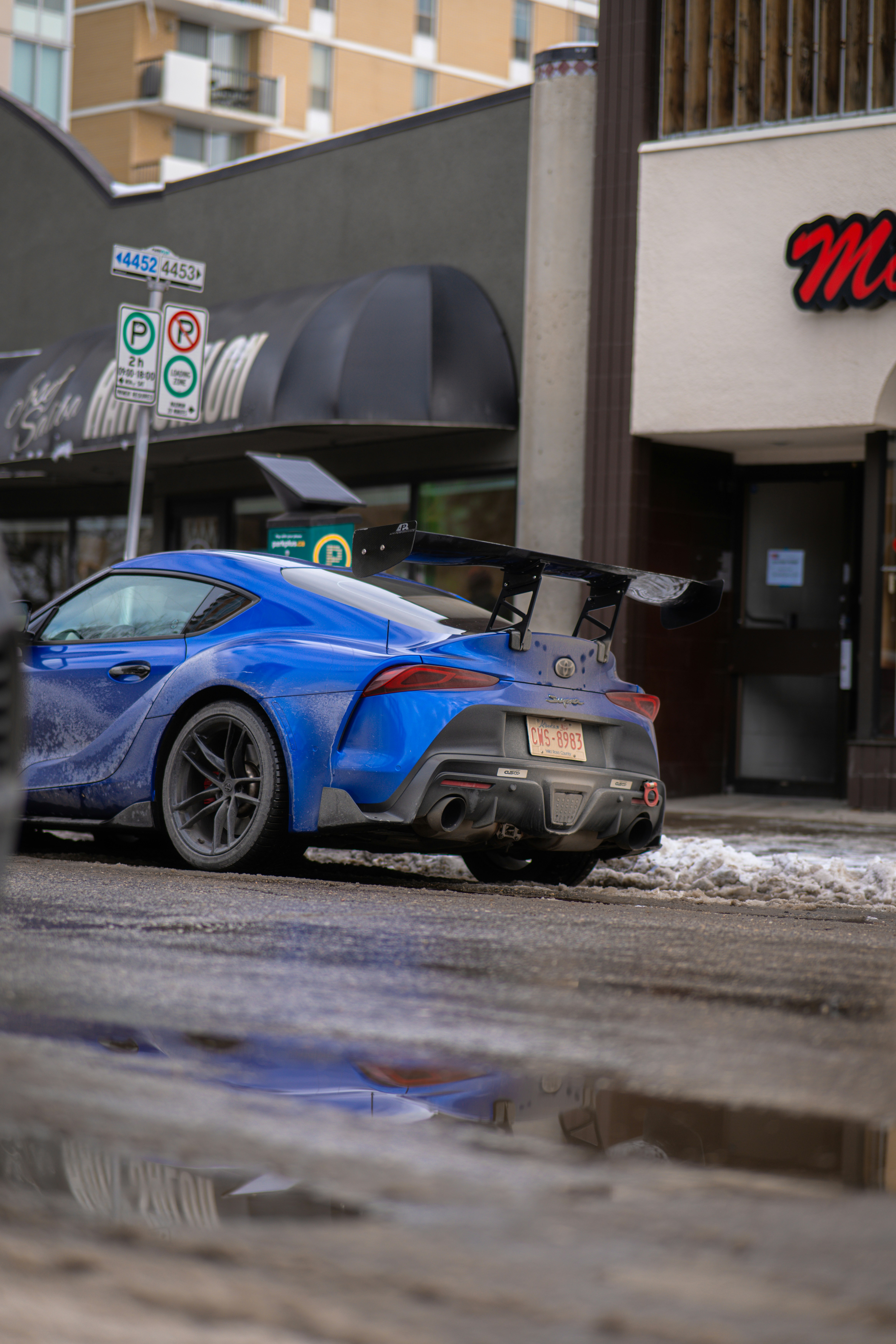 Blue Sports Car Reversing Past a Wet Urban Street