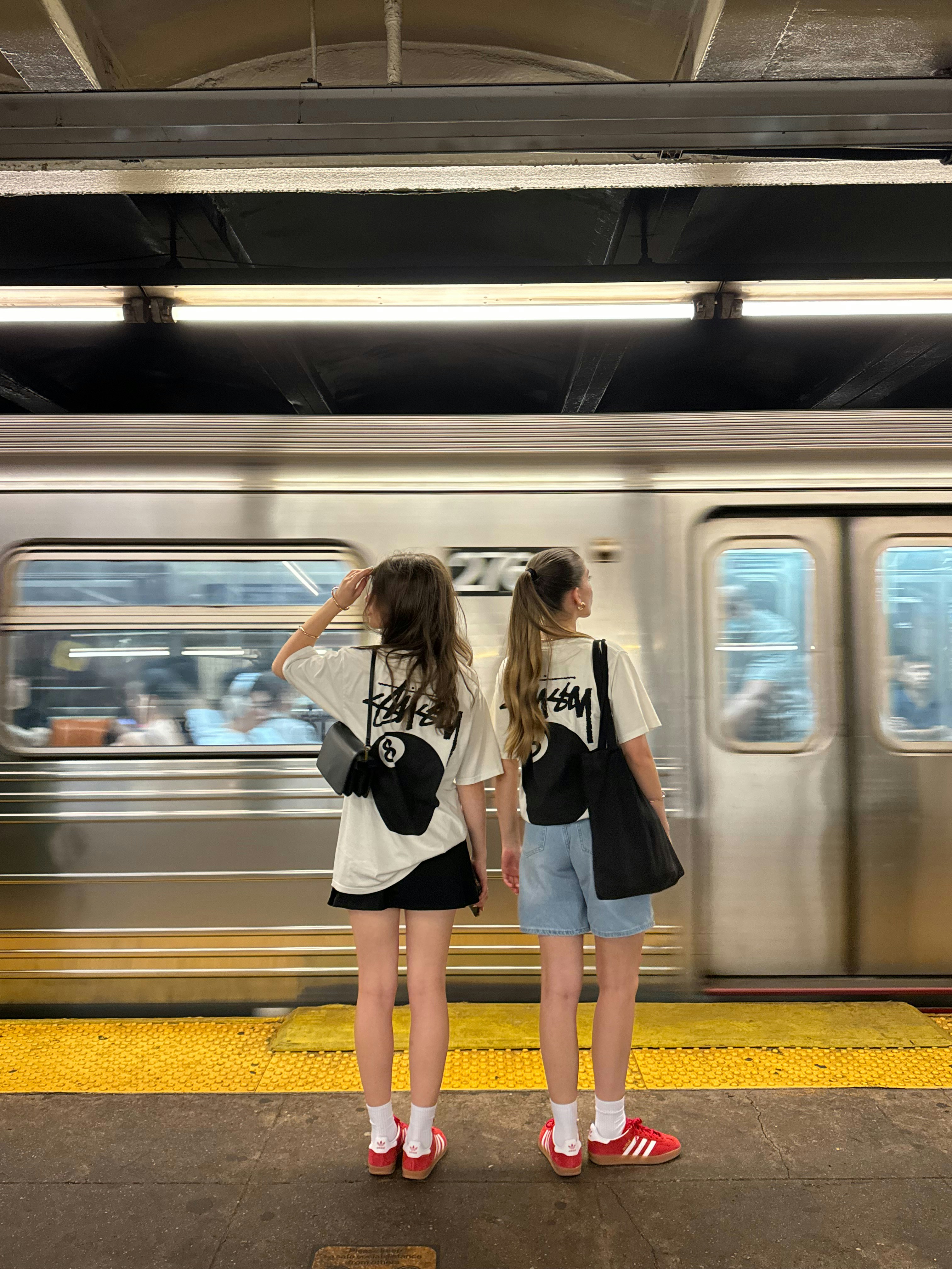 Two Girls on a Subway Platform Alertly Waiting as the Train Whizzes By