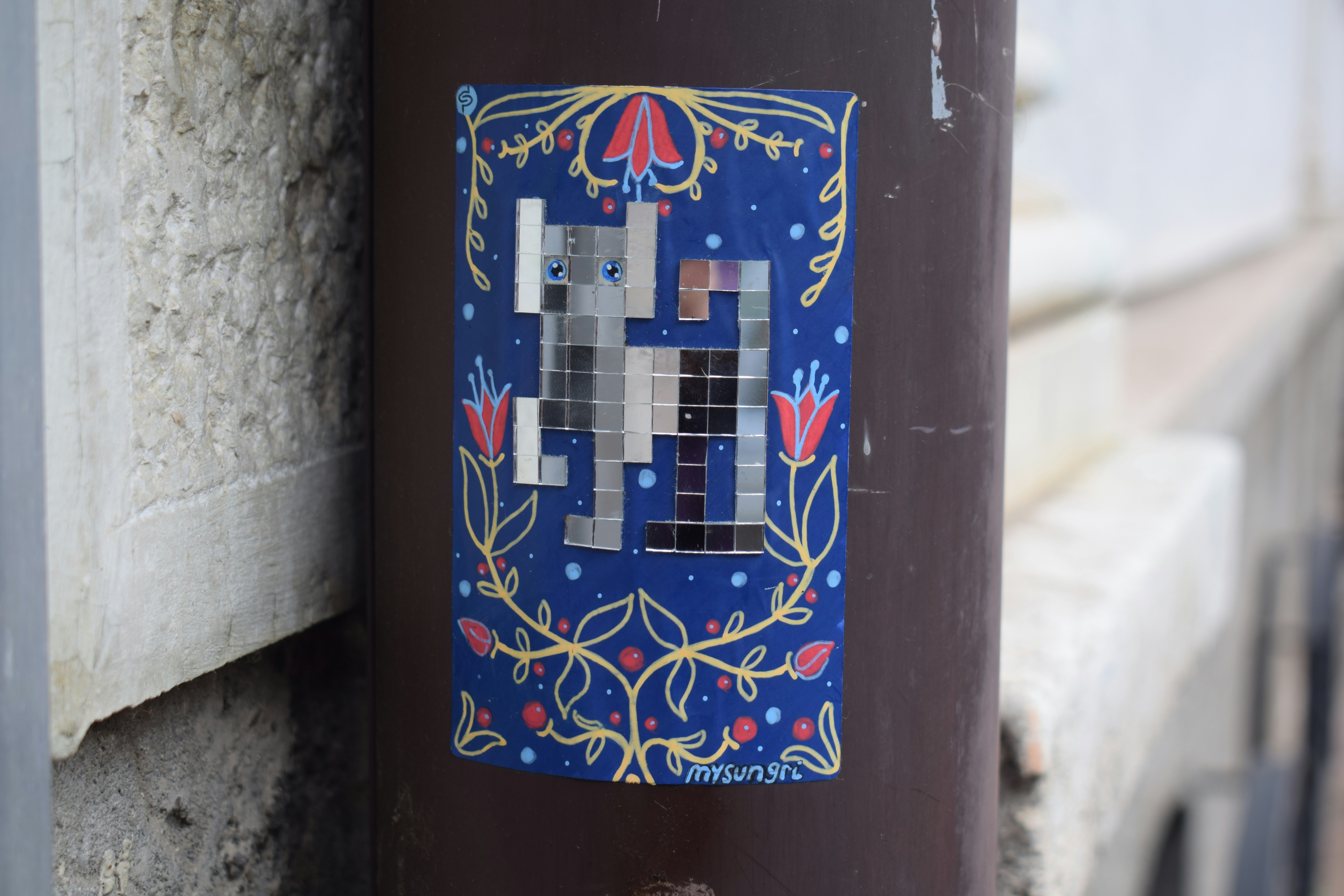 A Pixelated Cat Adorns a Blue Ornate Card on a Brown Post