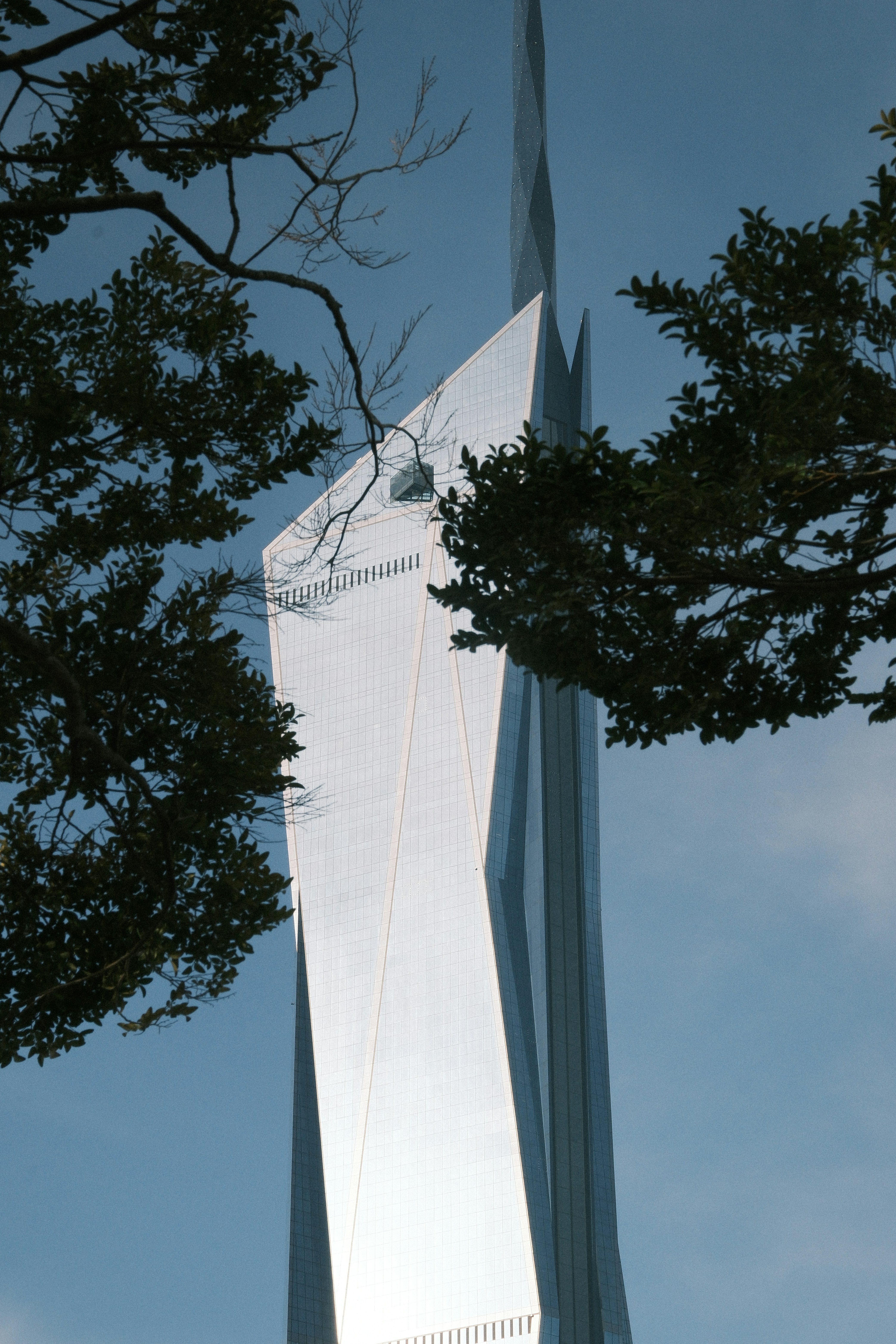 A close-up of a sleek skyscraper in Kuala Lumpur, showcasing its modern design and glass surface reflecting the surrounding cityscape. The tower stands tall, blending contemporary architecture with urban life.