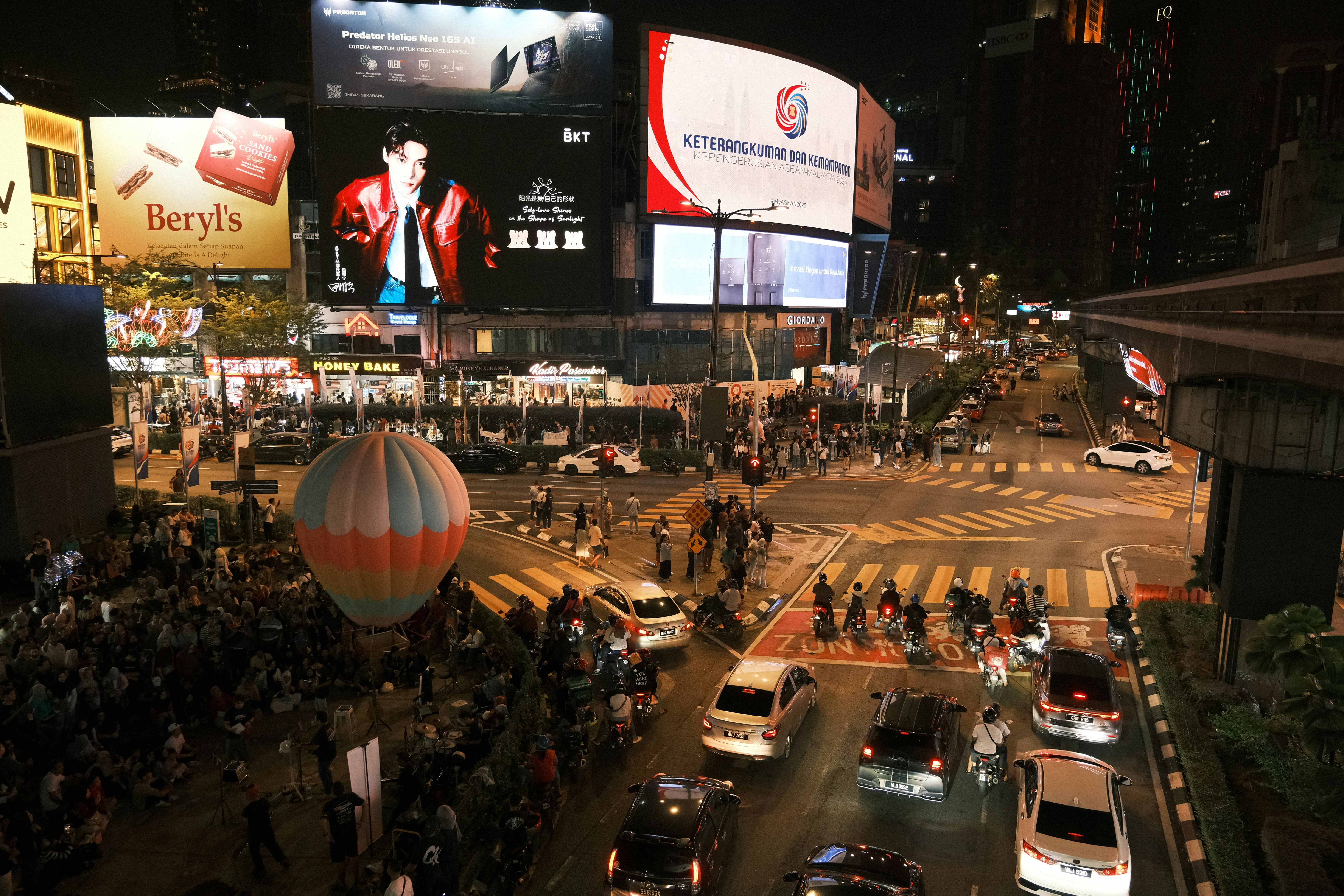 A view from above Bukit Bintang, showcasing the busy streets of Kuala Lumpur with glowing billboards and bustling pedestrians. The image captures the energy of the city at night, highlighting its vibrant atmosphere and urban life.