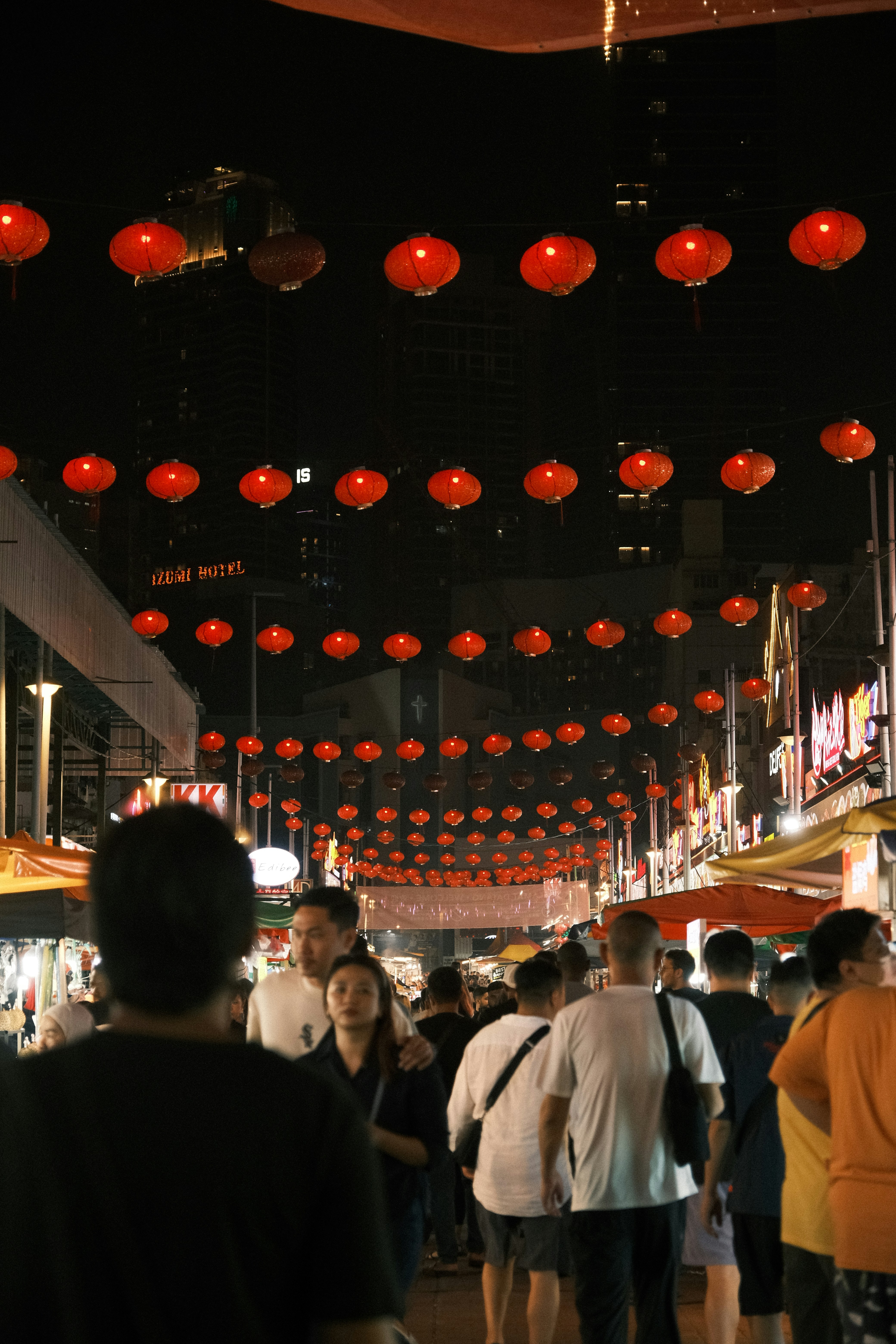 A vibrant night scene in Jalan Alor, Kuala Lumpur, with colorful red lanterns hanging above the bustling street full of people and food stalls. The lively atmosphere is a perfect blend of culture, street food, and urban energy.