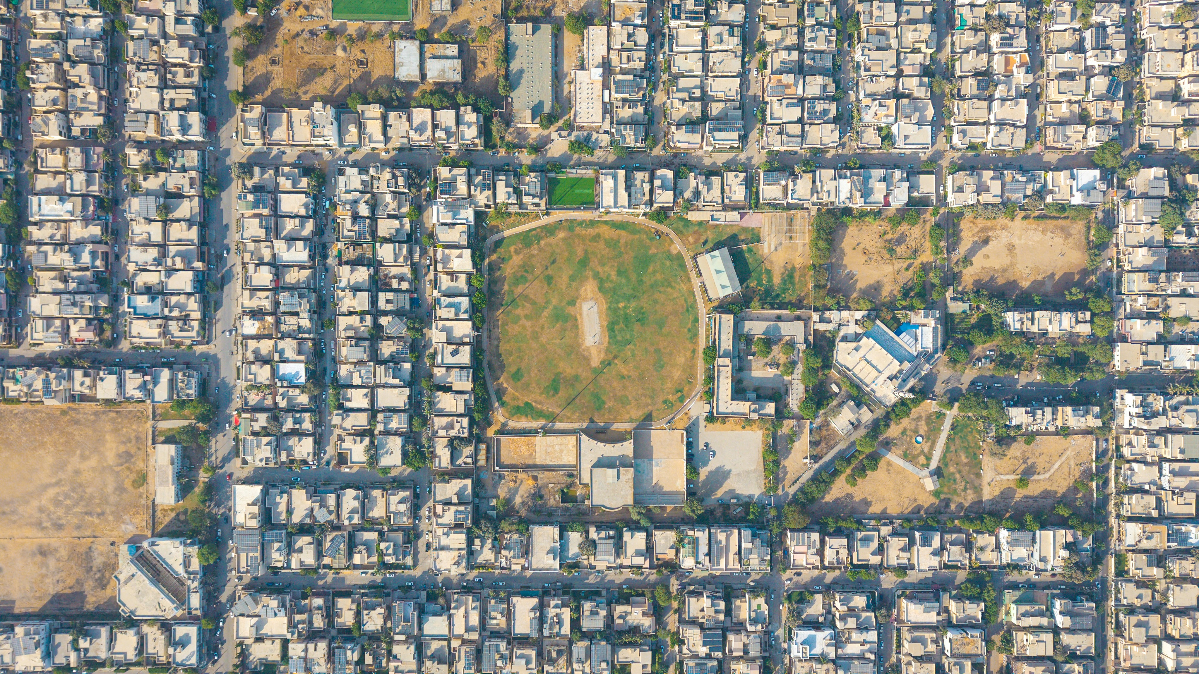 A clean aerial view of a Karachi neighborhood showing a cricket ground surrounded by tightly packed urban housing.