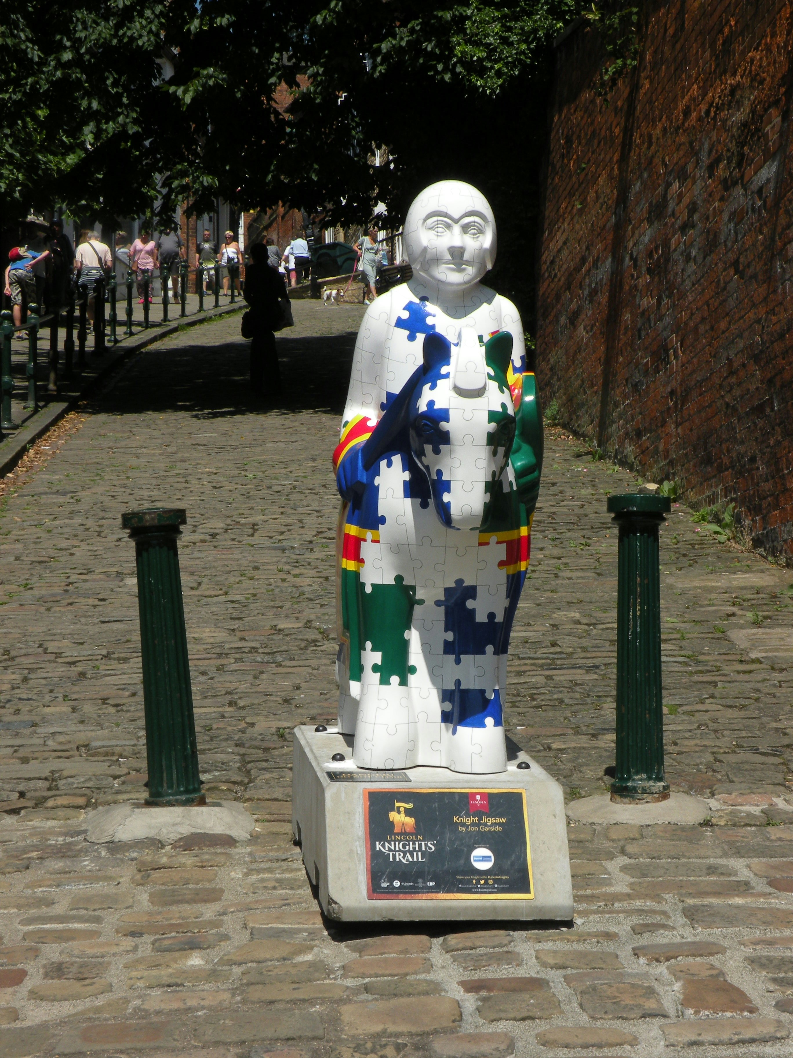 Statue decorated with colorful puzzle pieces on cobblestone street.