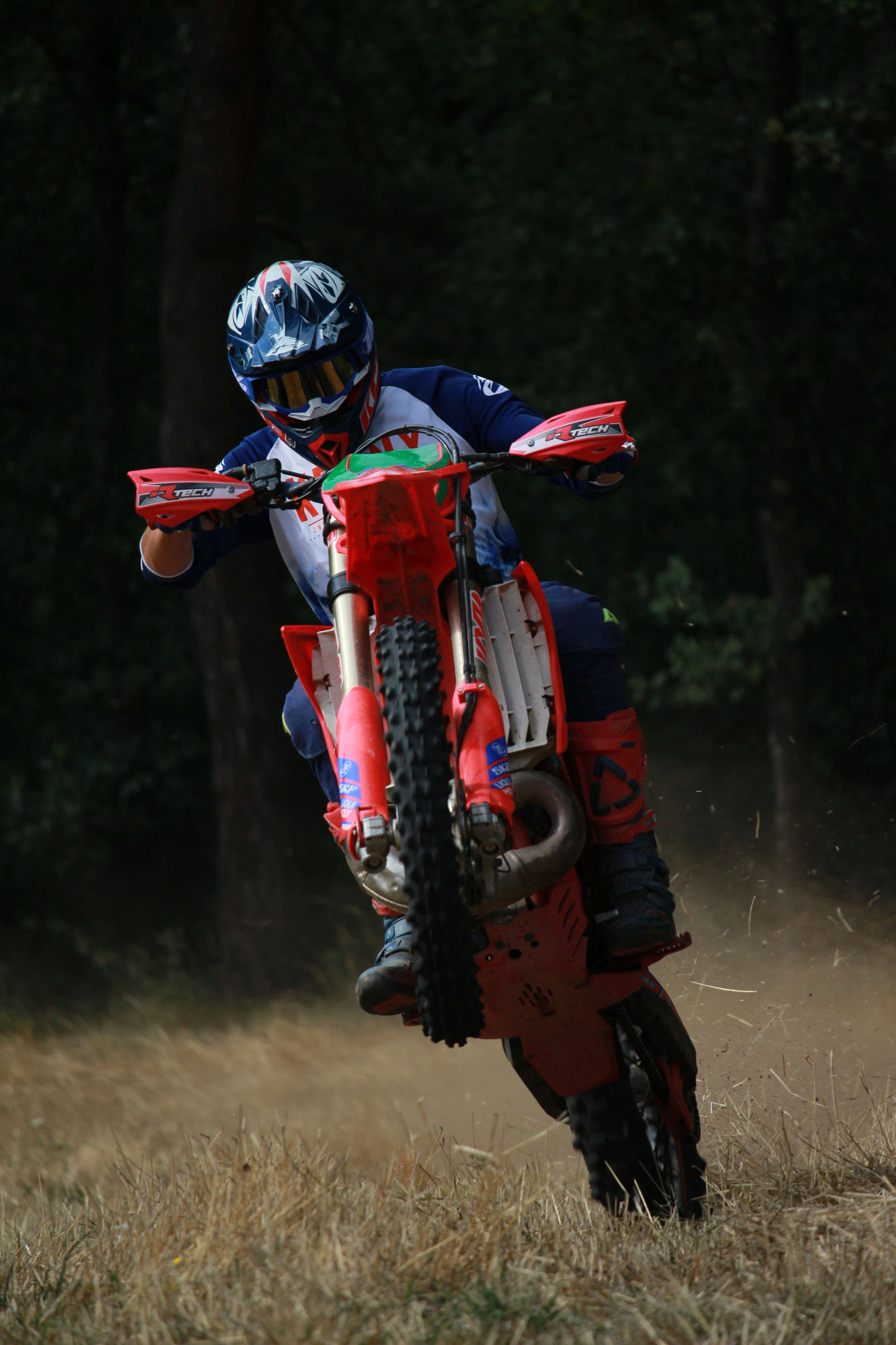 Motorcyclist riding a red dirt bike through dry grass.