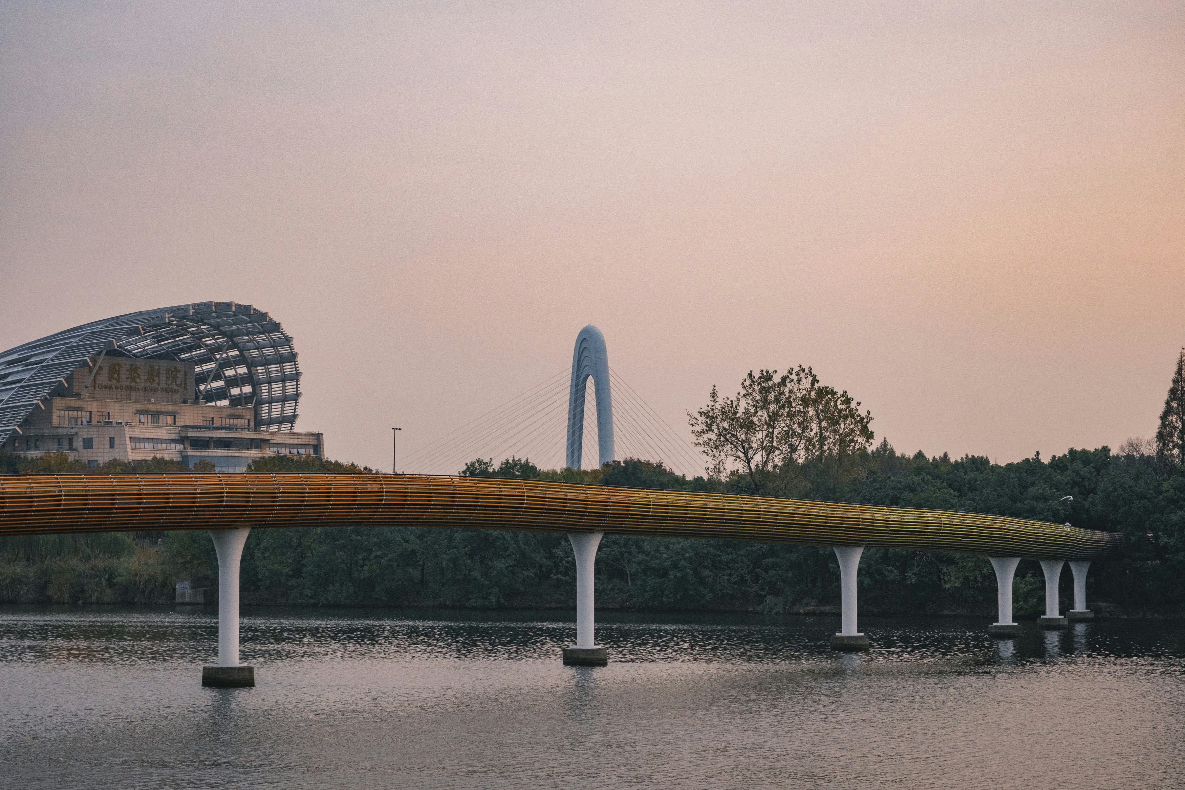Bridge over tranquil waters with a futuristic arch skyline at dusk