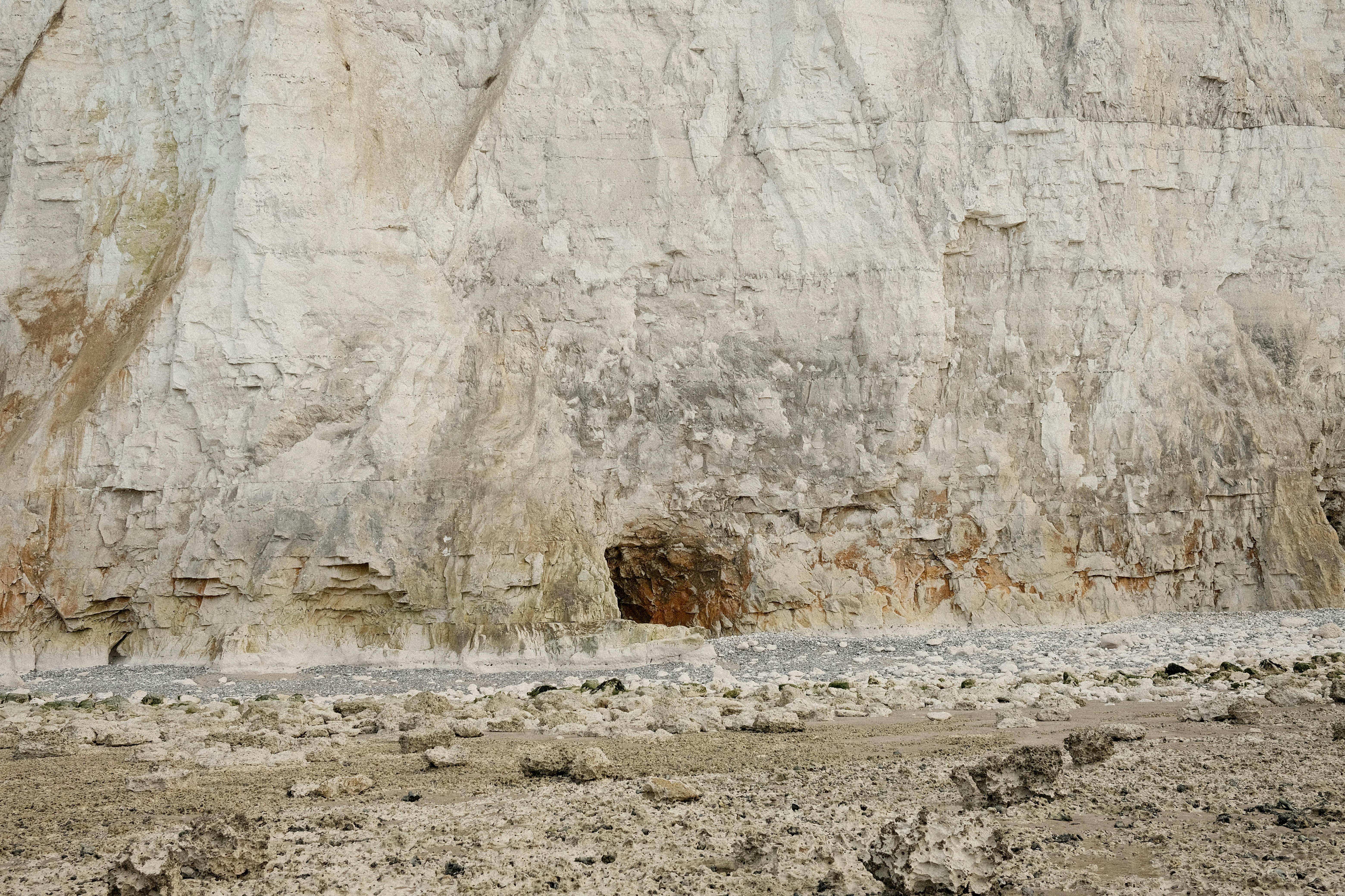 White cliff face with weathered sea bank and small cave opening
