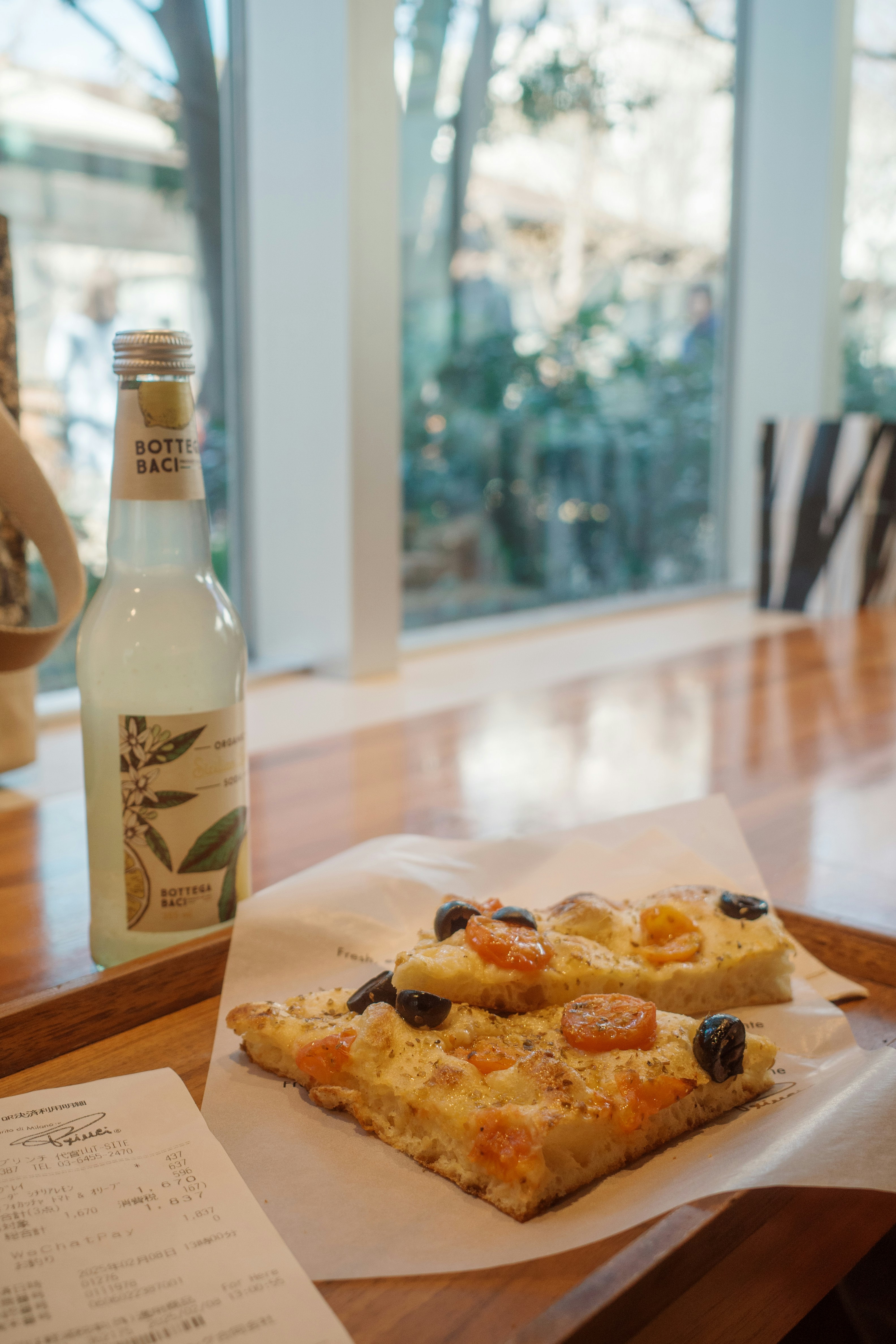 Sliced stone fruit and olives on a rustic tray with a bottle of white wine by a sunlit window