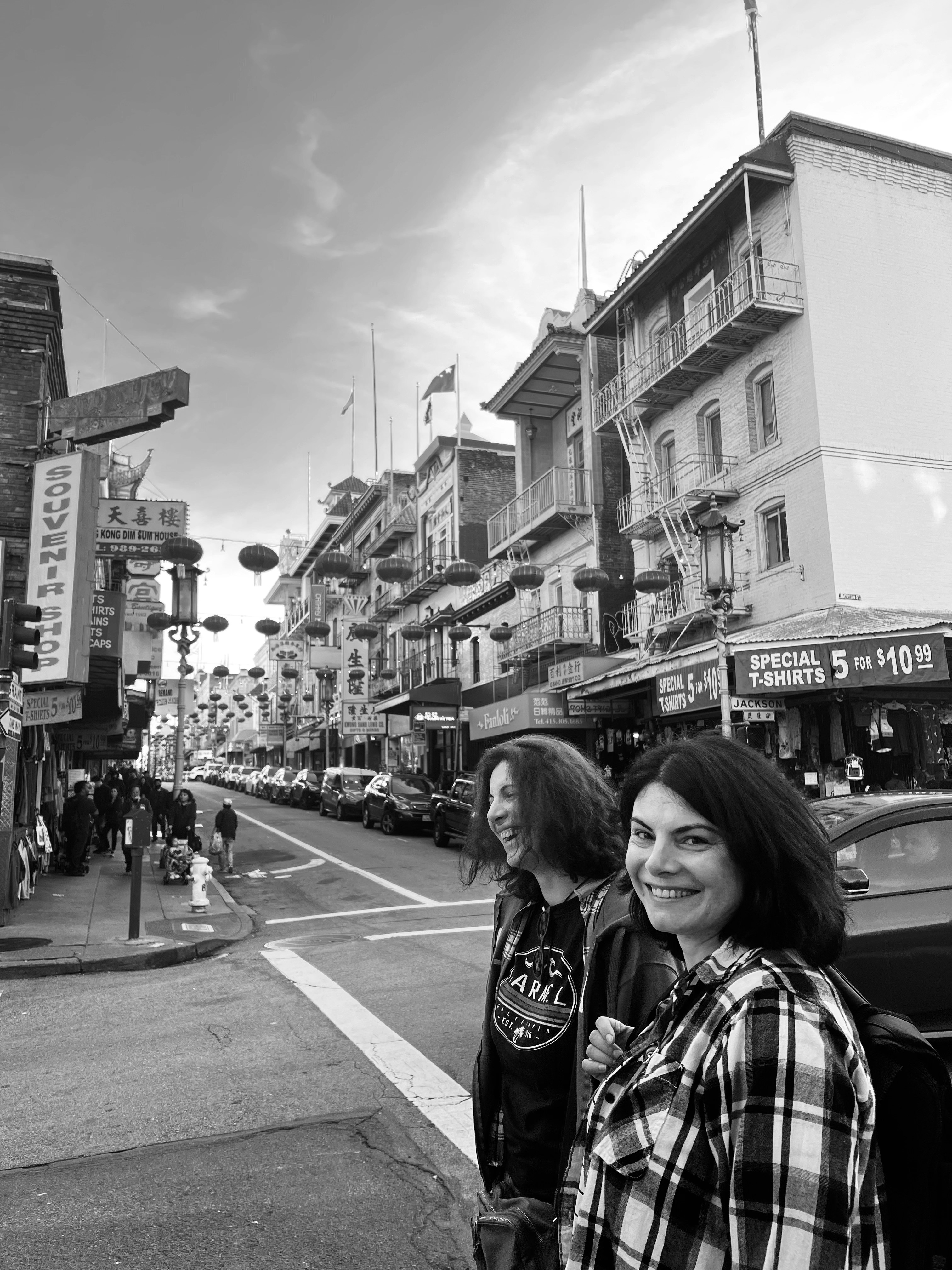 Smiling duo in a sunlit Chinatown-like street scene