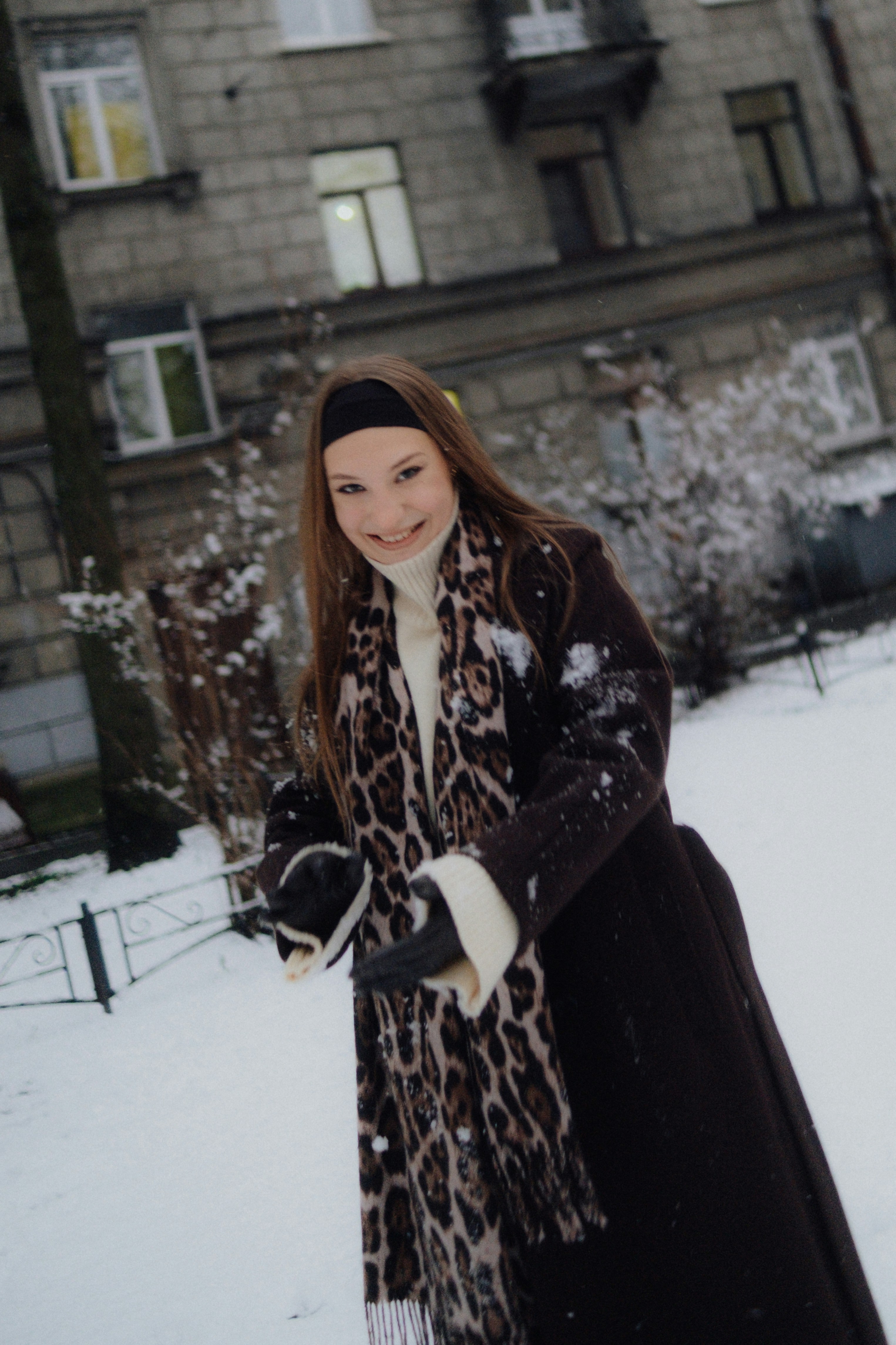 Winter Smile: A Woman in Leopard Scarf Against A Snowy City Backdrop