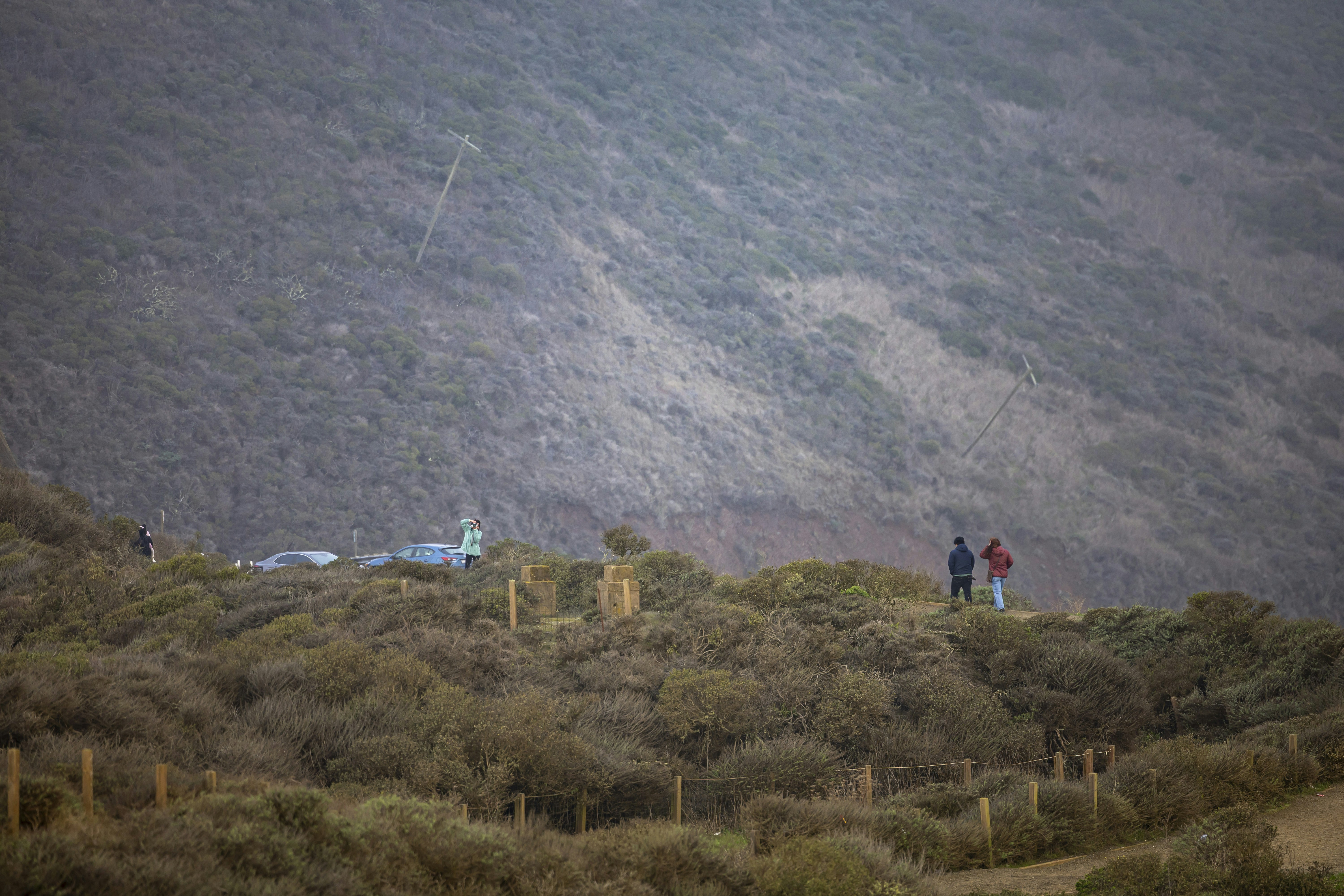 Two hikers on a windswept ridge beneath a distant cratered hillside
