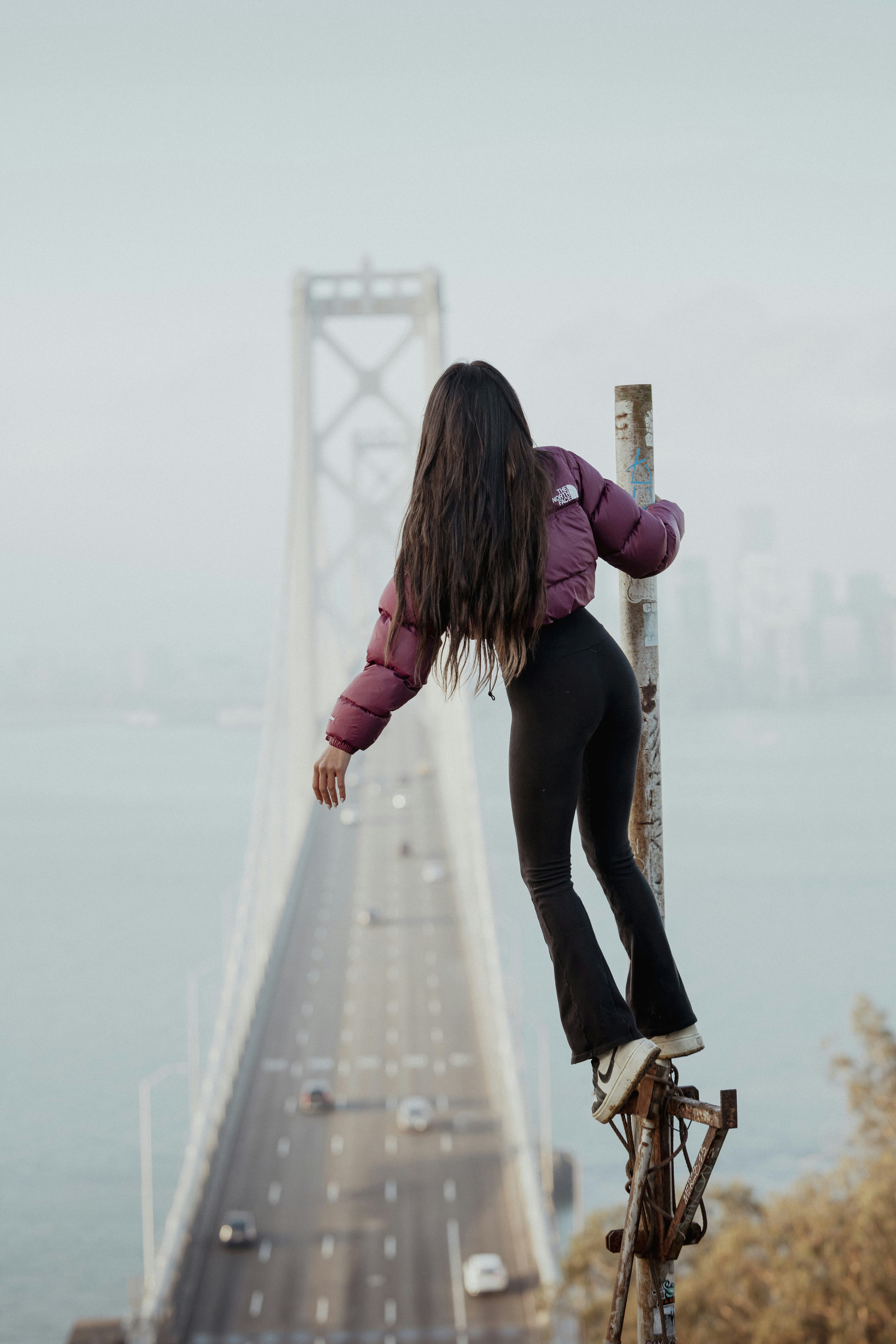 Woman balancing on pole with bridge behind