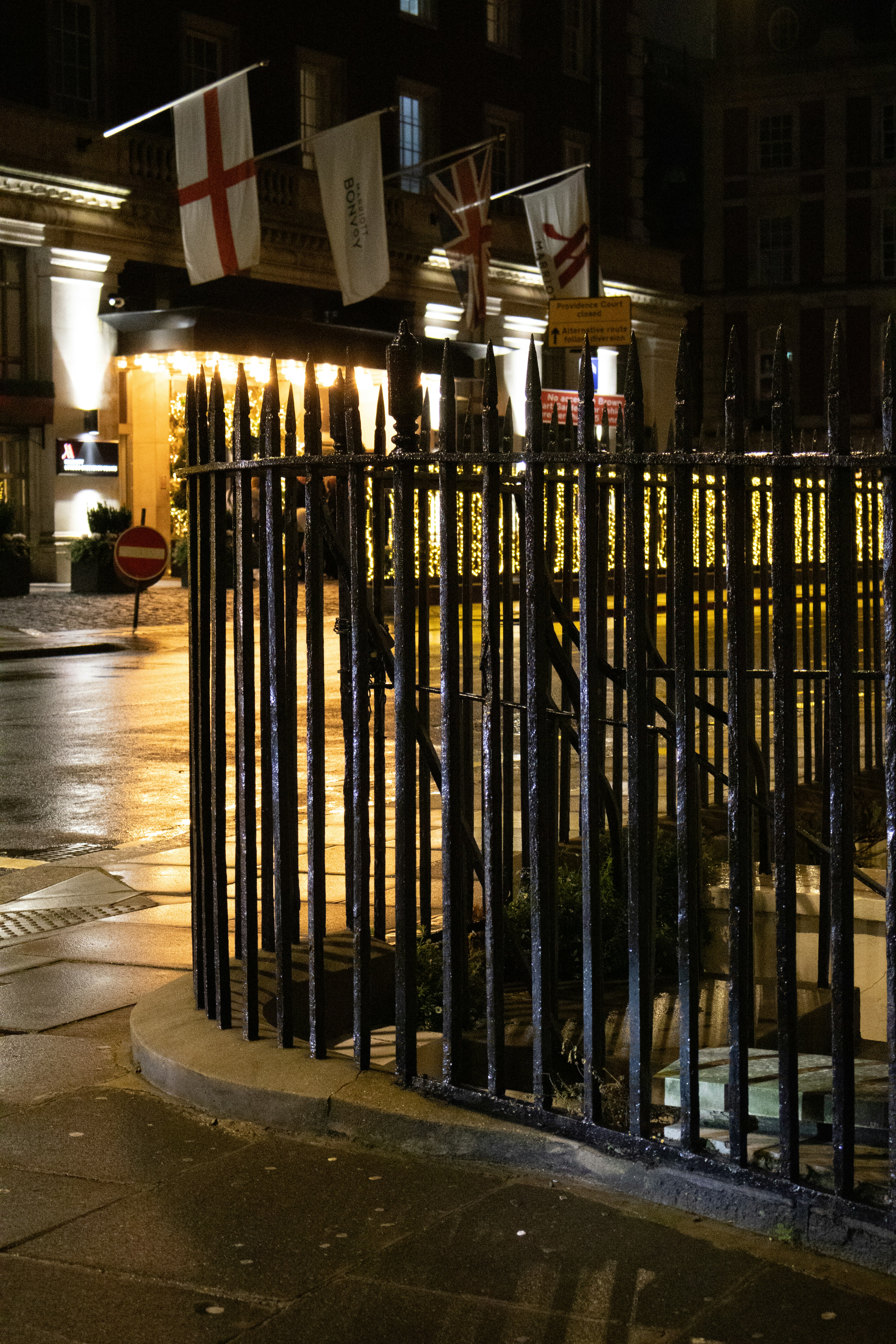 Iron Spikes and Warm Light: Night at the Corner Gate