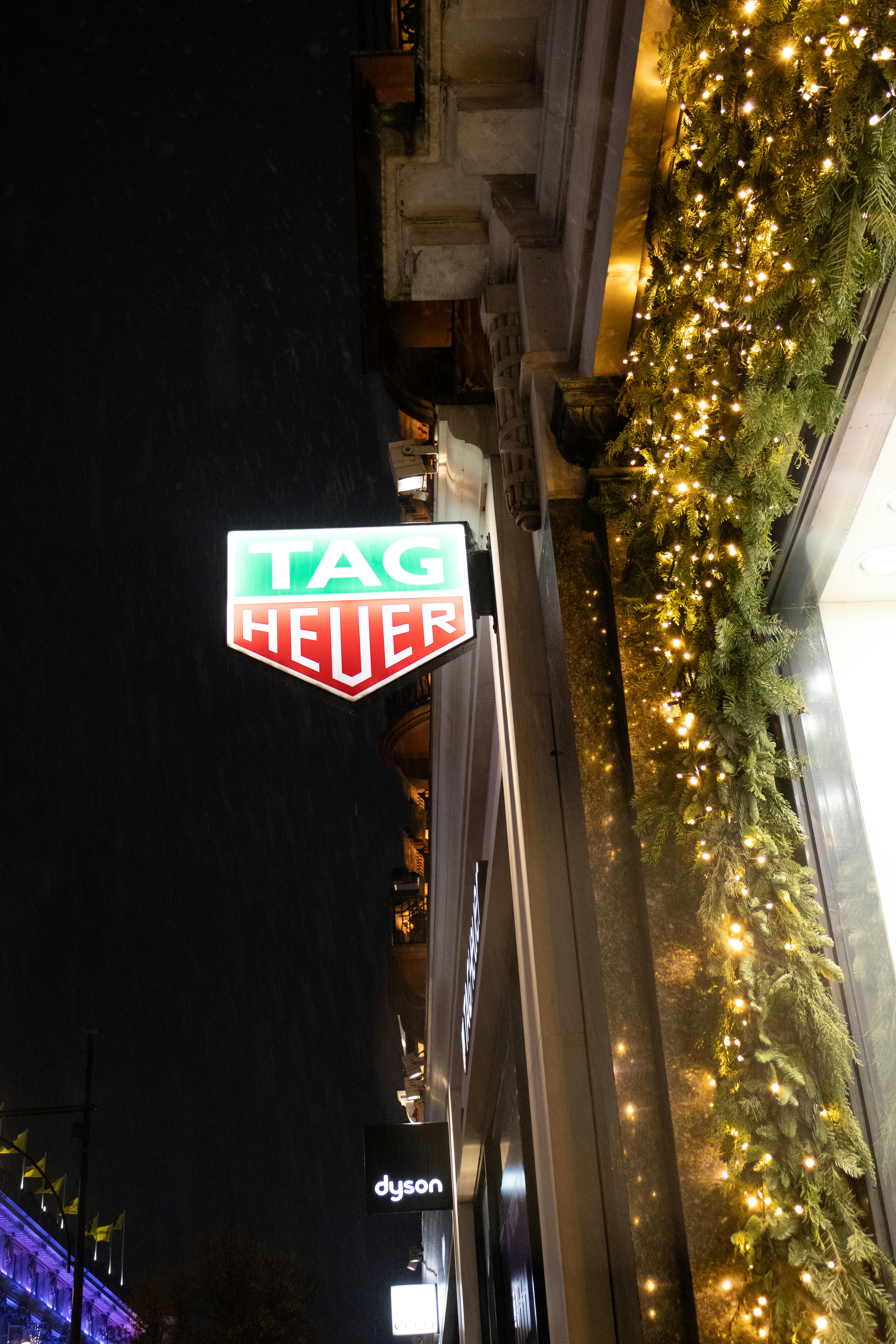 Neon TAG Heuer Sign Framed by Festive Gleam Along a City Facade
