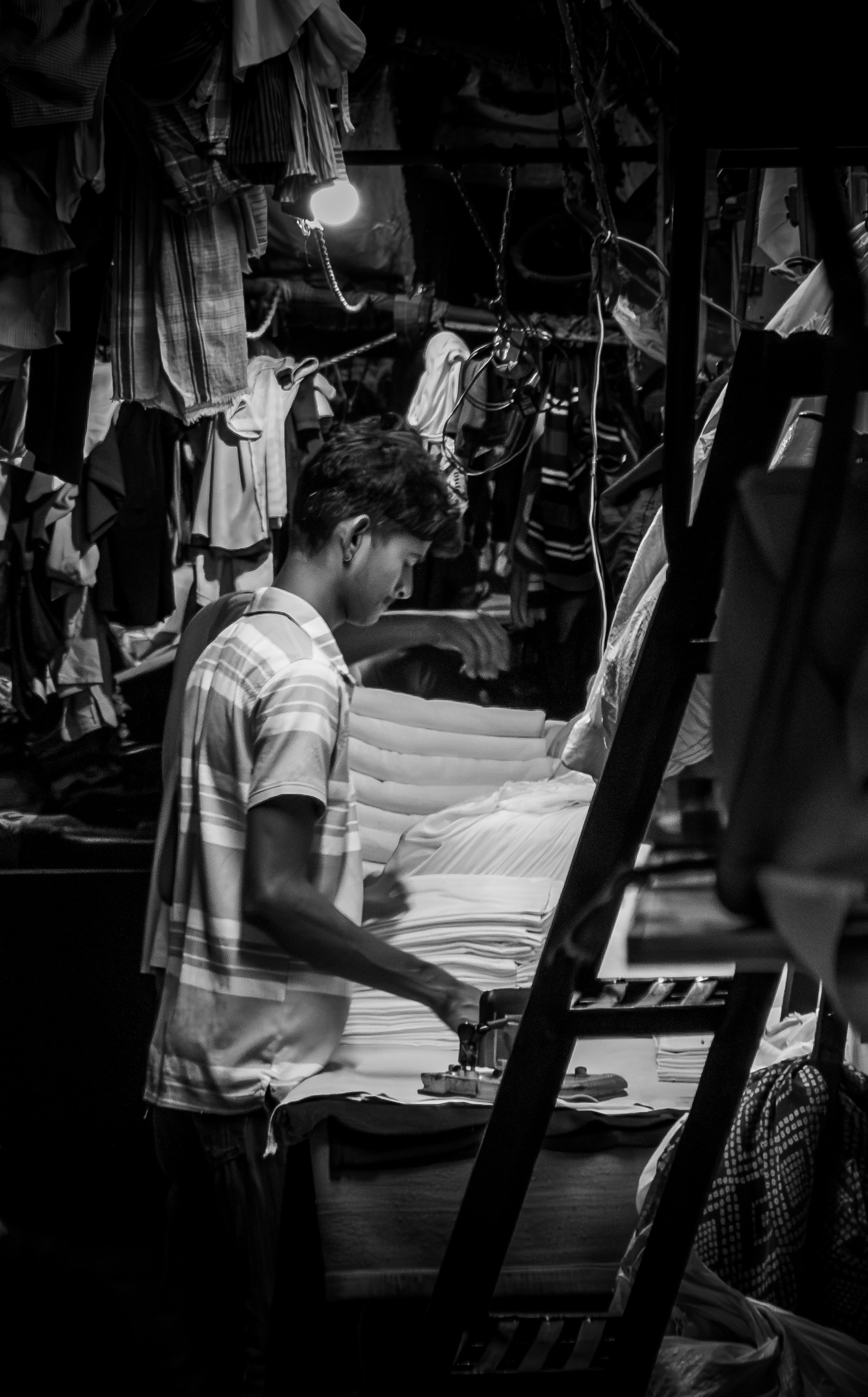 A young man standing next to a tall stack of freshly laundered white linens, diligently ironing the garments using an industrial iron.